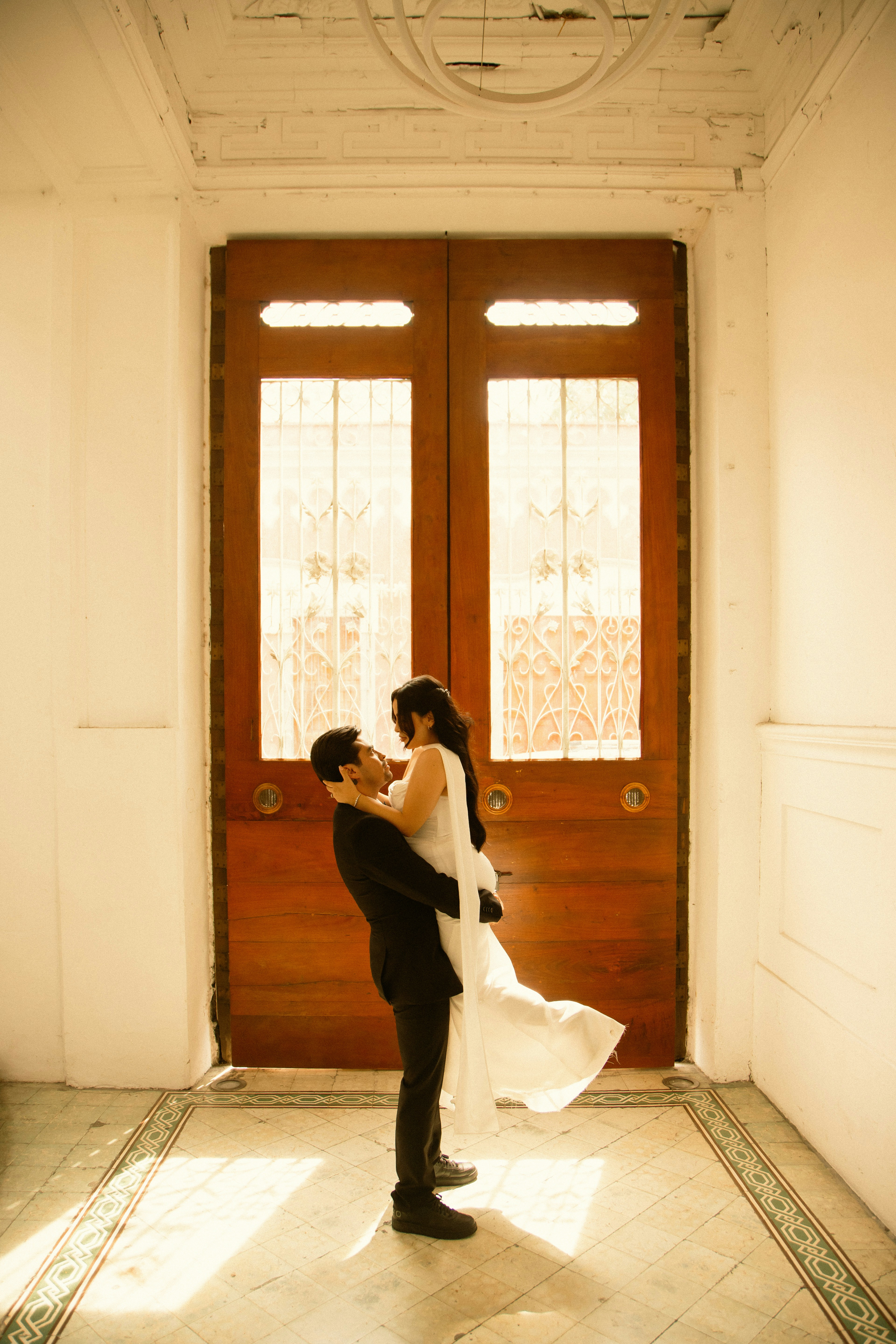 Couple sharing an intimate moment in front of grand wooden doors, illuminated by soft light. The scene captures the essence of romance and commitment.