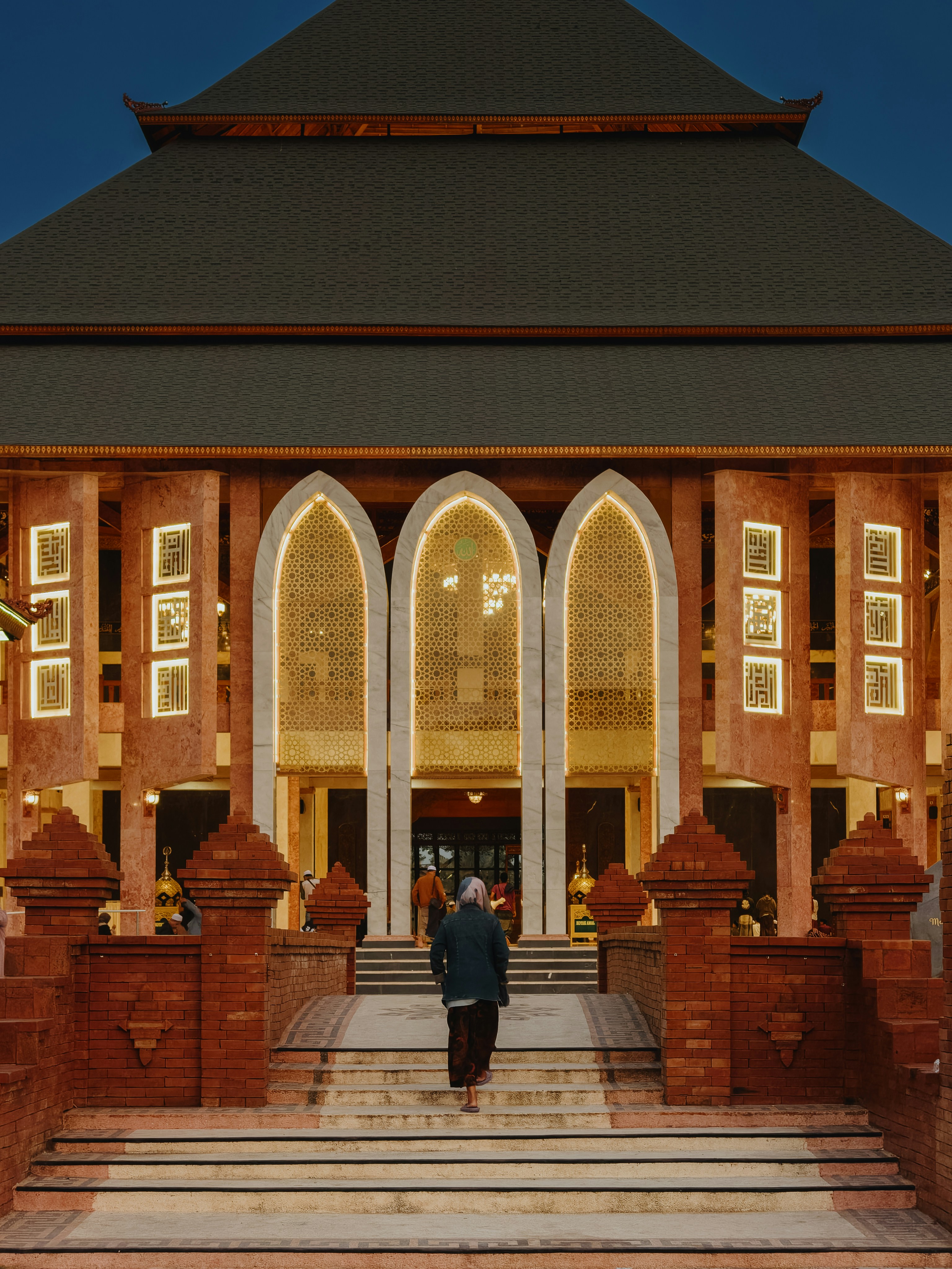 A person ascends the grand steps of an intricately designed building, showcasing elegant arches and warm lighting that highlight its architectural beauty.
