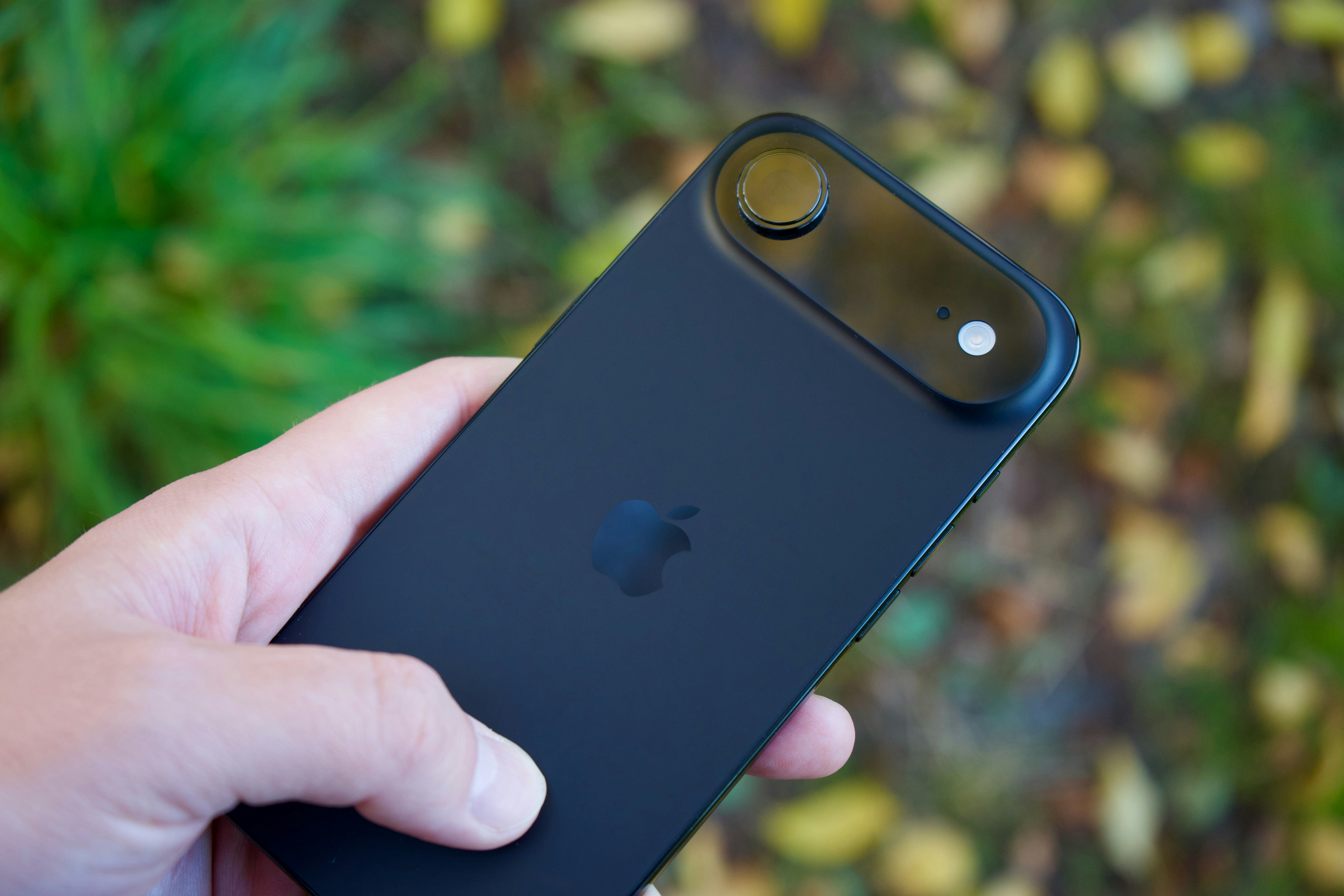 A hand holding a sleek black smartphone against a backdrop of autumn leaves, showcasing the device's minimalist design.