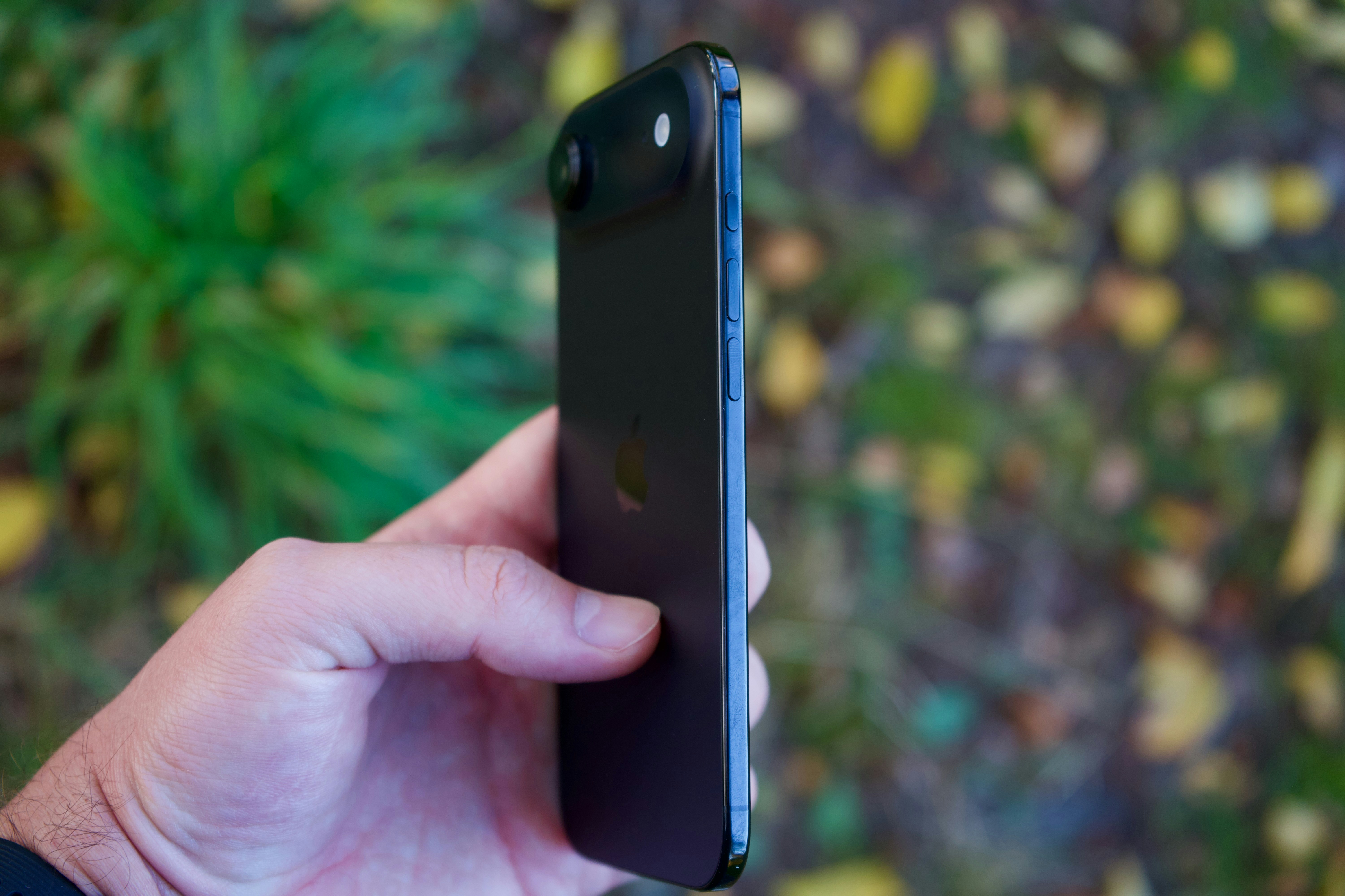 Hand holding a sleek smartphone against a backdrop of autumn leaves, showcasing the blend of technology and nature.