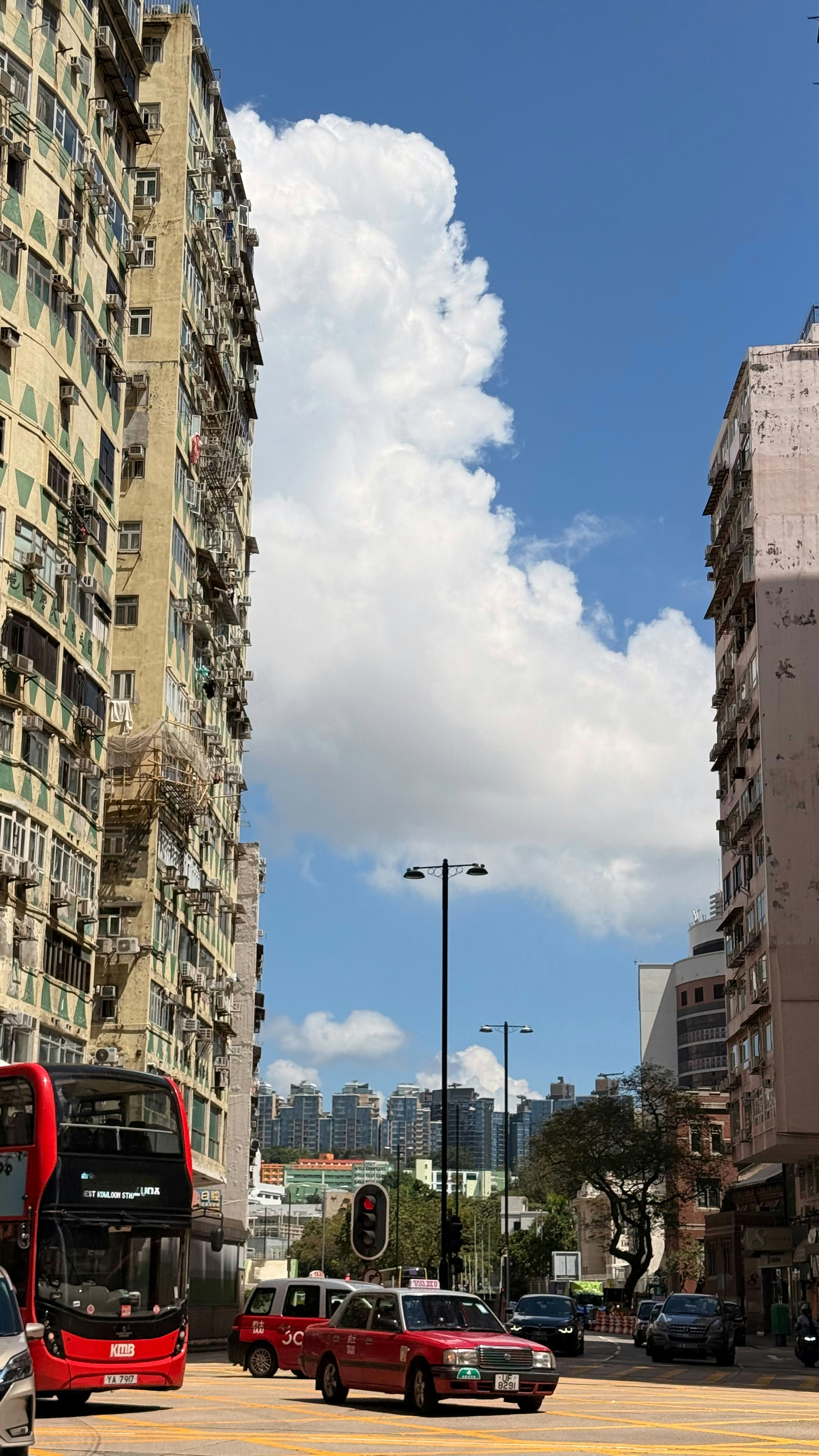 Vibrant cityscape featuring a mix of towering buildings and a bright blue sky with fluffy clouds. Buses and cars navigate the bustling street below.