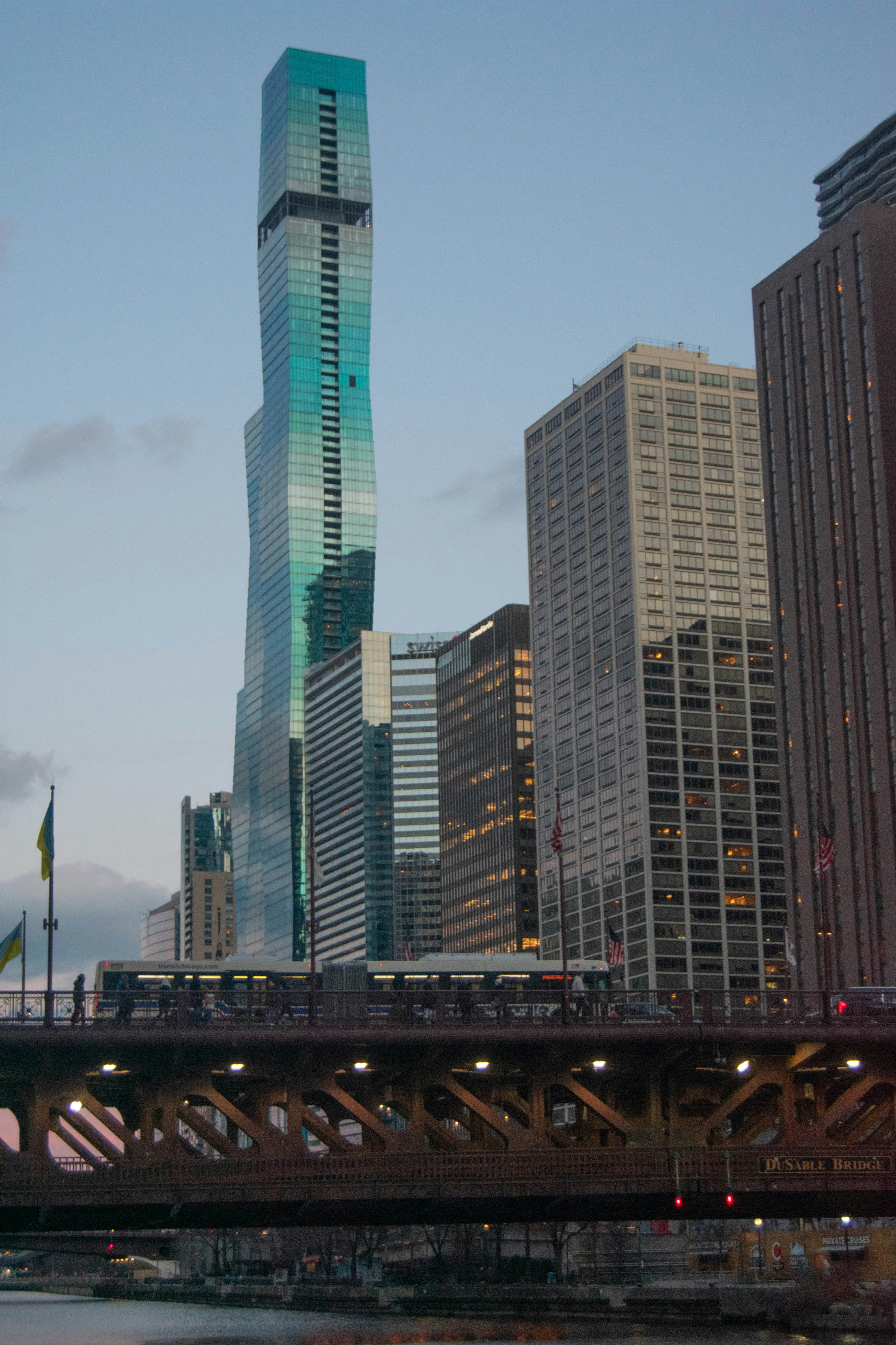 A striking skyscraper reflecting the evening sky, surrounded by a blend of contemporary architecture along the waterway.