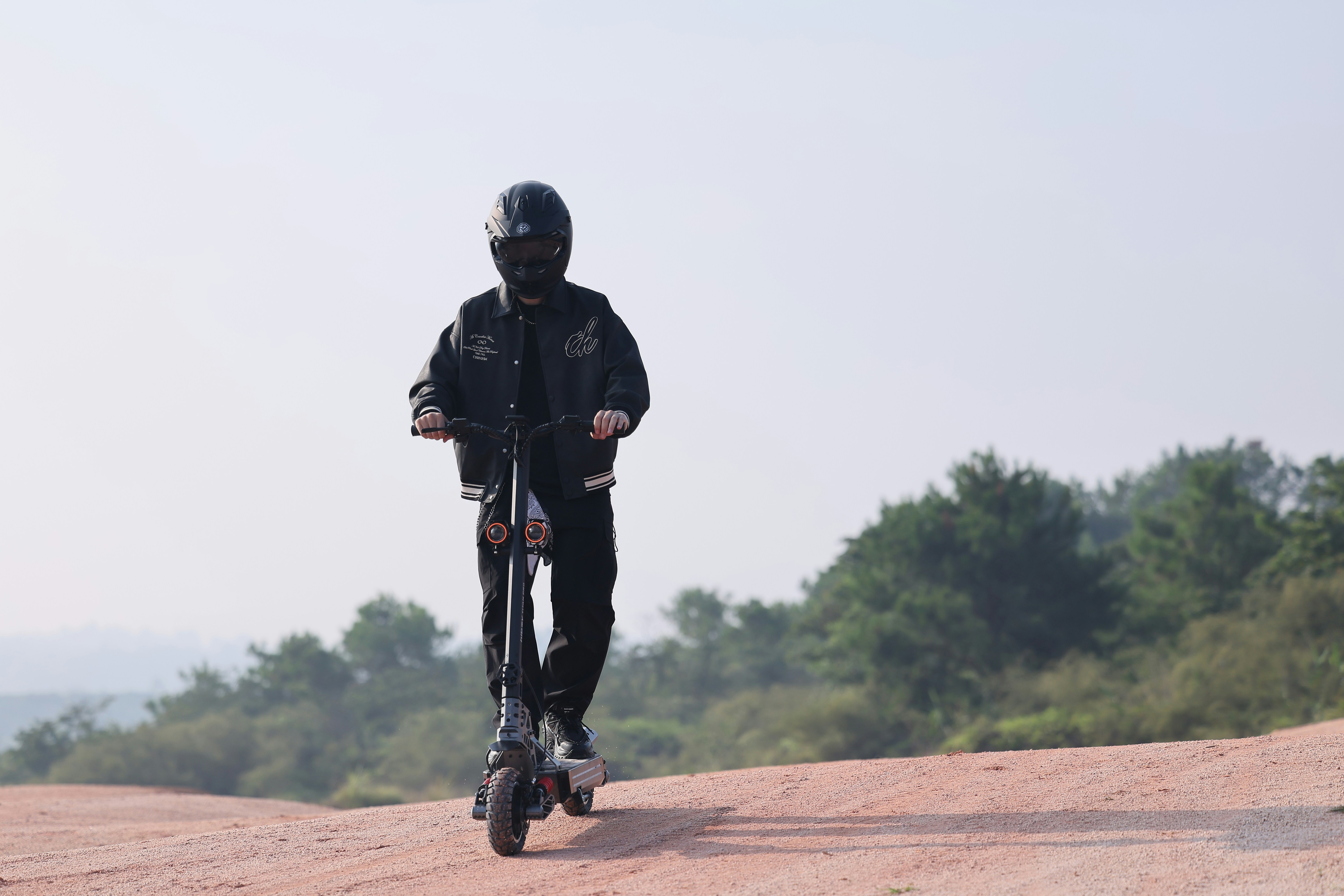 Individual riding an electric scooter along a dirt path surrounded by greenery.