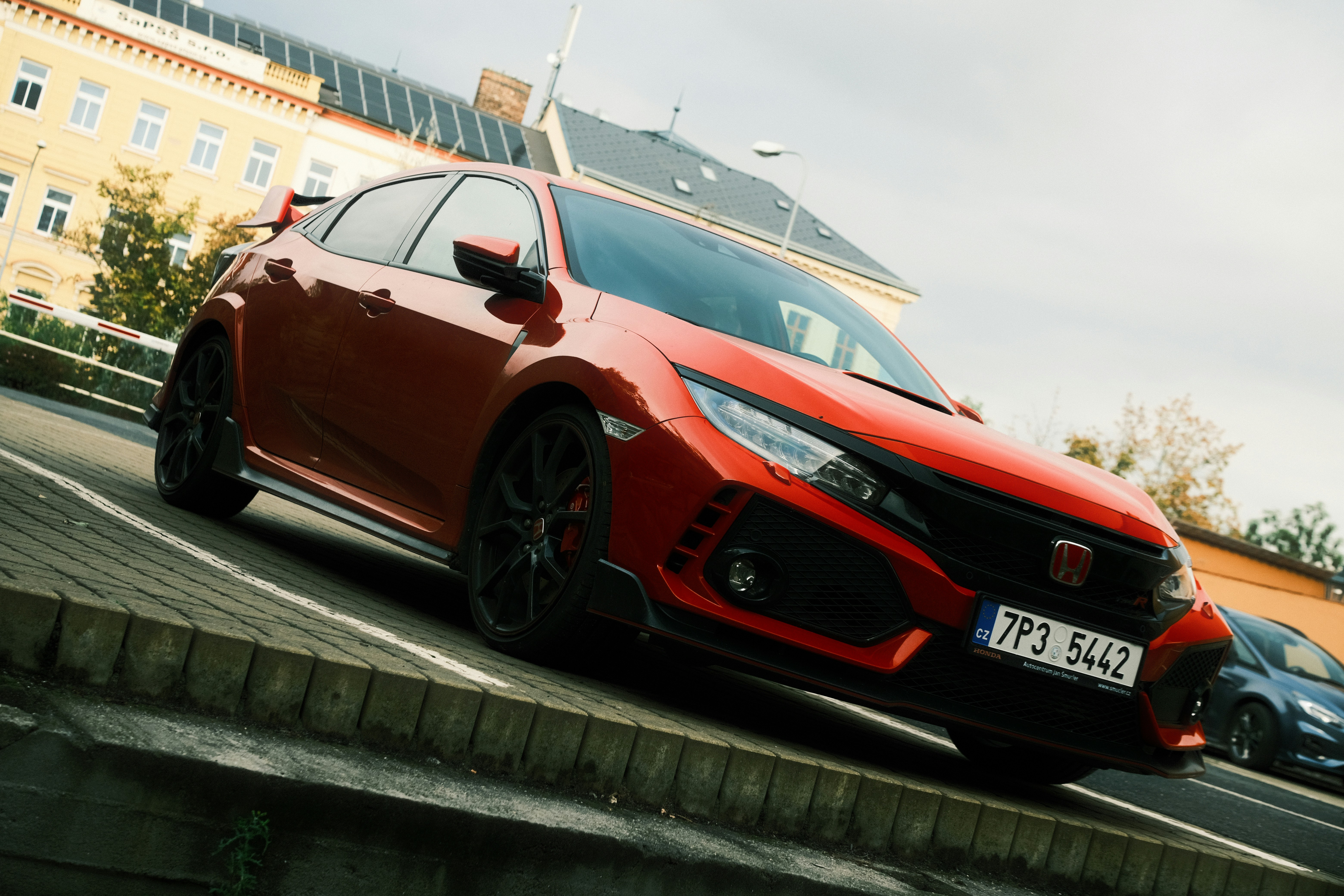 A sleek red Honda Civic Type R parked at an angle, showcasing its aggressive styling and sporty features against an urban backdrop.