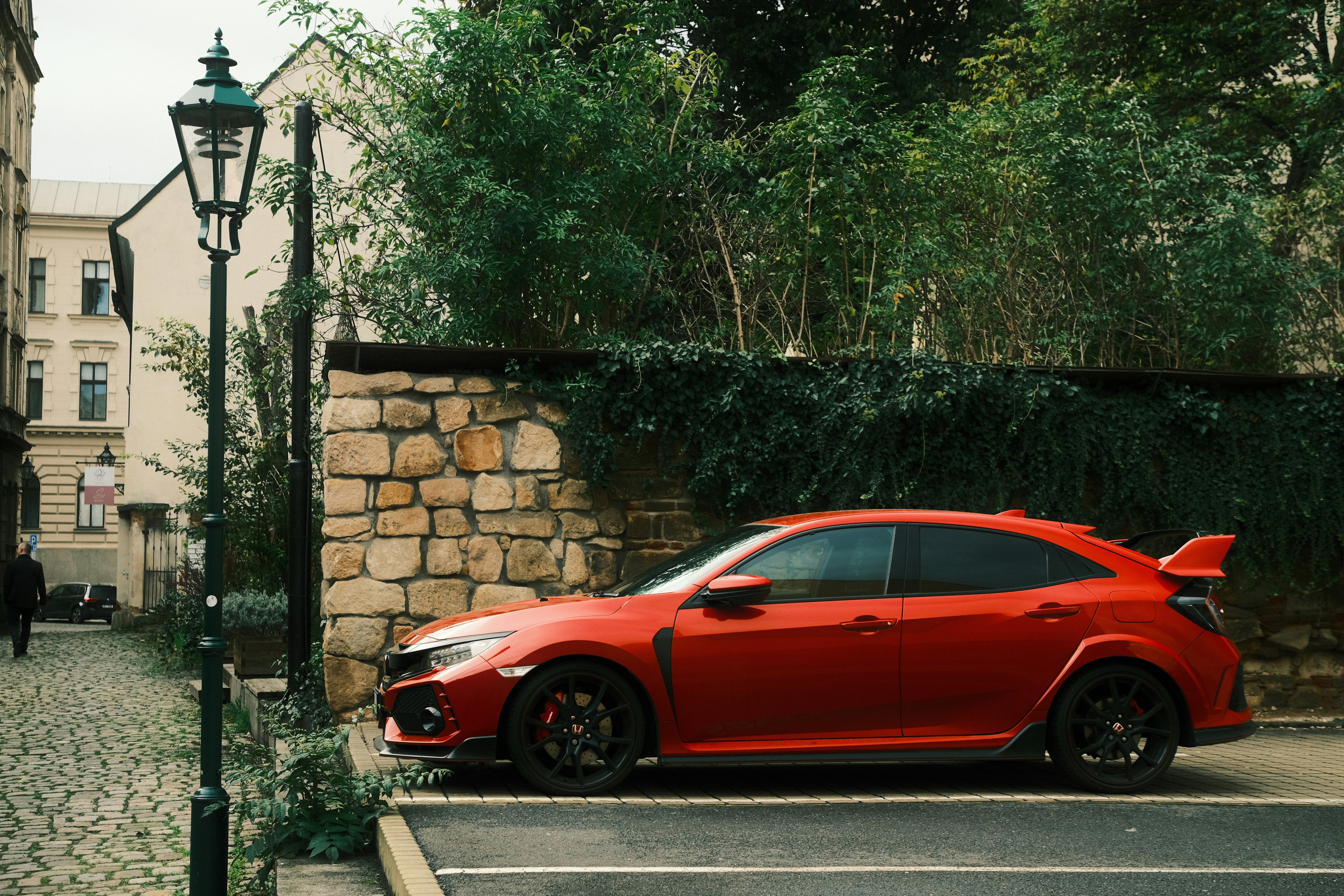 Crimson Hatch on Cobblestones: A Red Car Framed by Ivy and Stone
