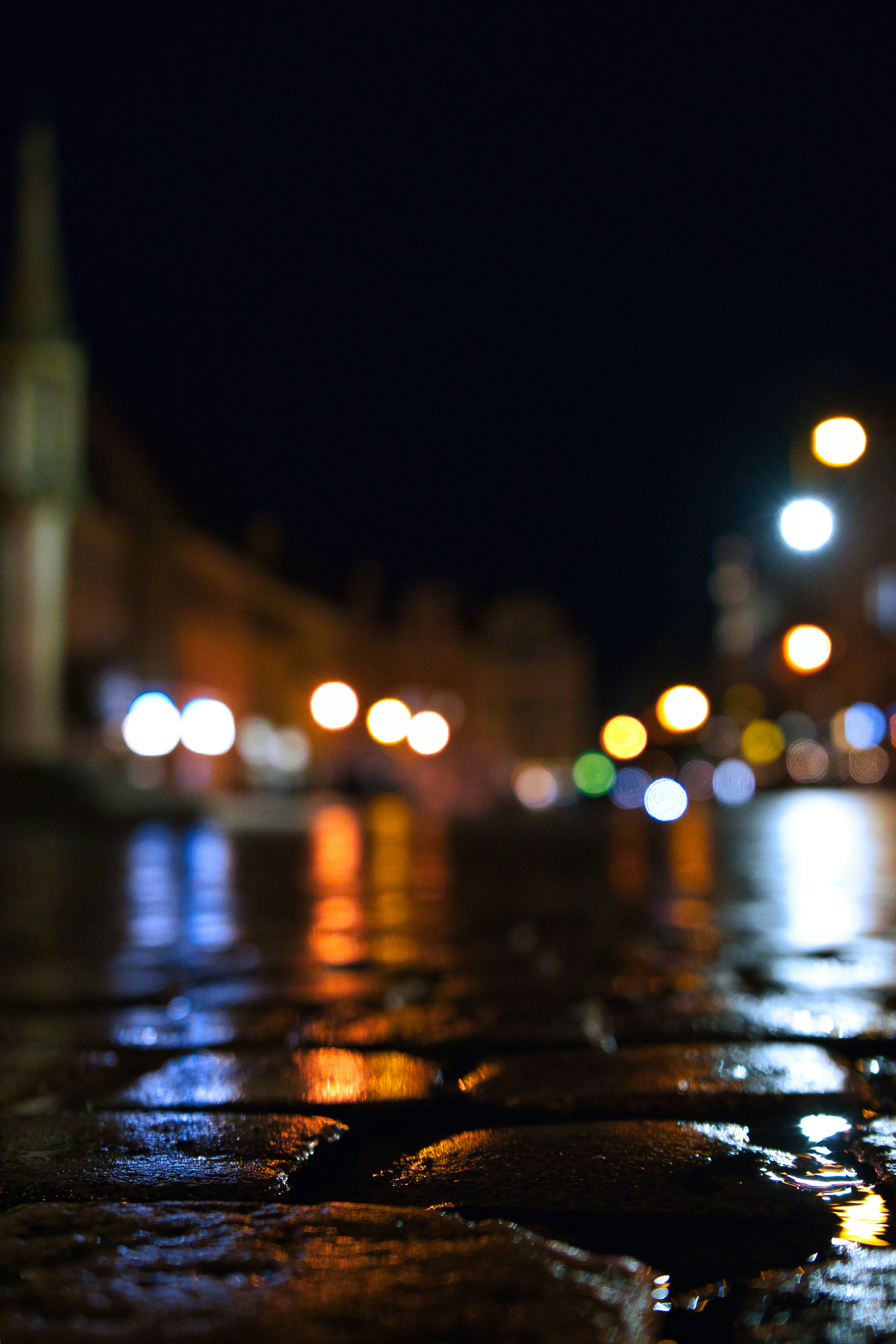 Wet cobblestone street reflecting city lights at night