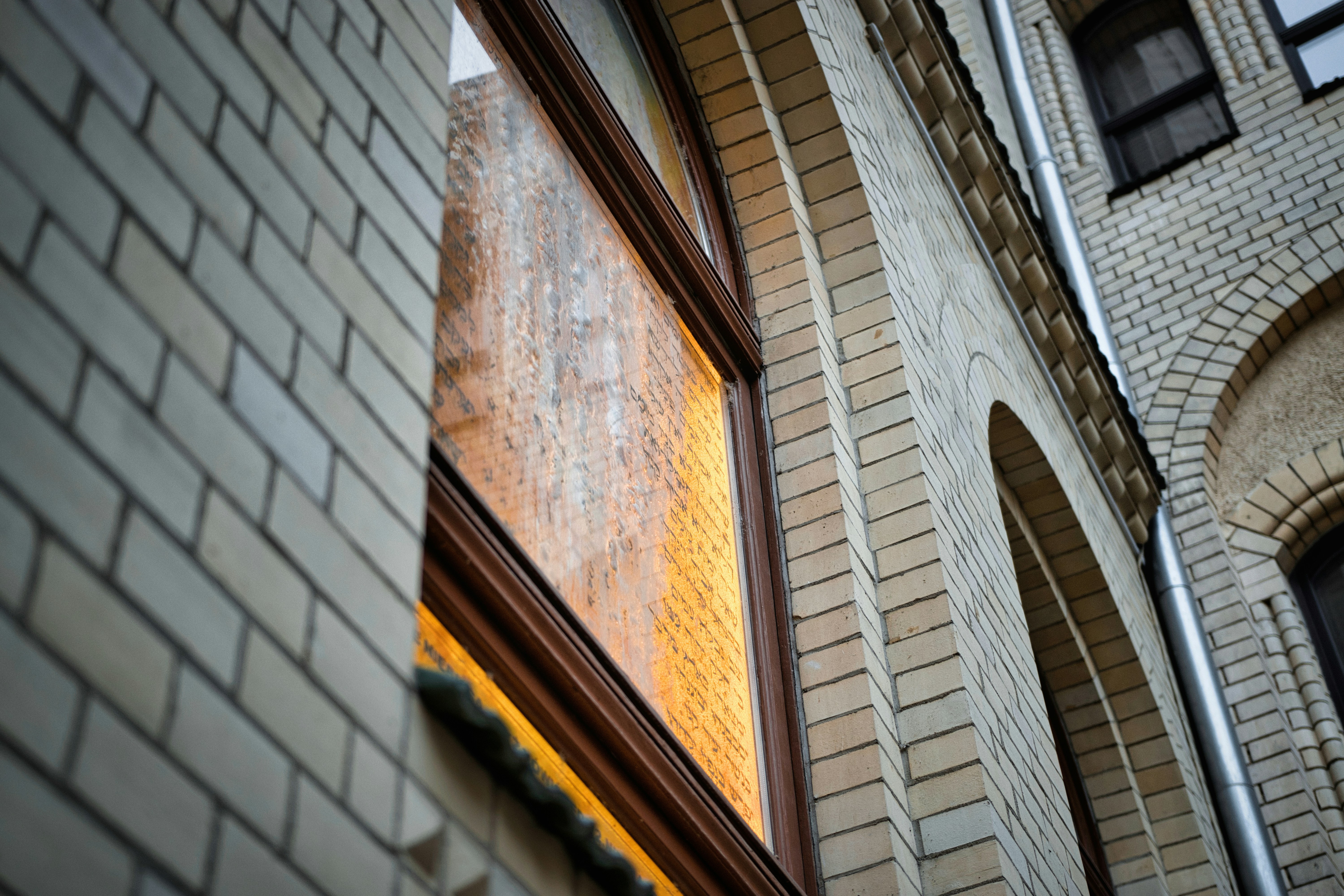 A close-up view of a textured window reflecting warm light against a brick wall, showcasing architectural details.