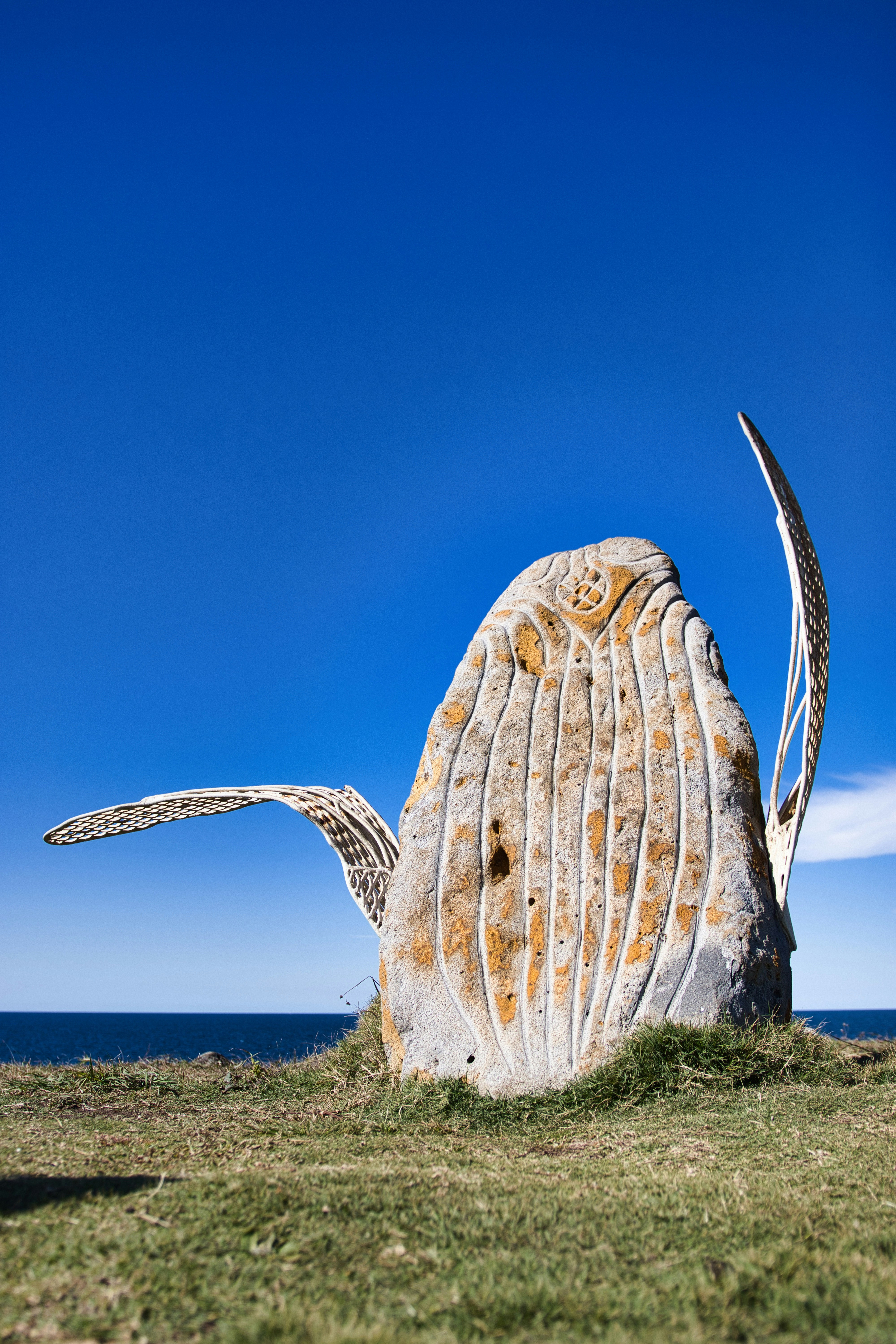 Winged Monolith by the Sea: A Coastal Sculpture Standing Against a Clear Blue Sky