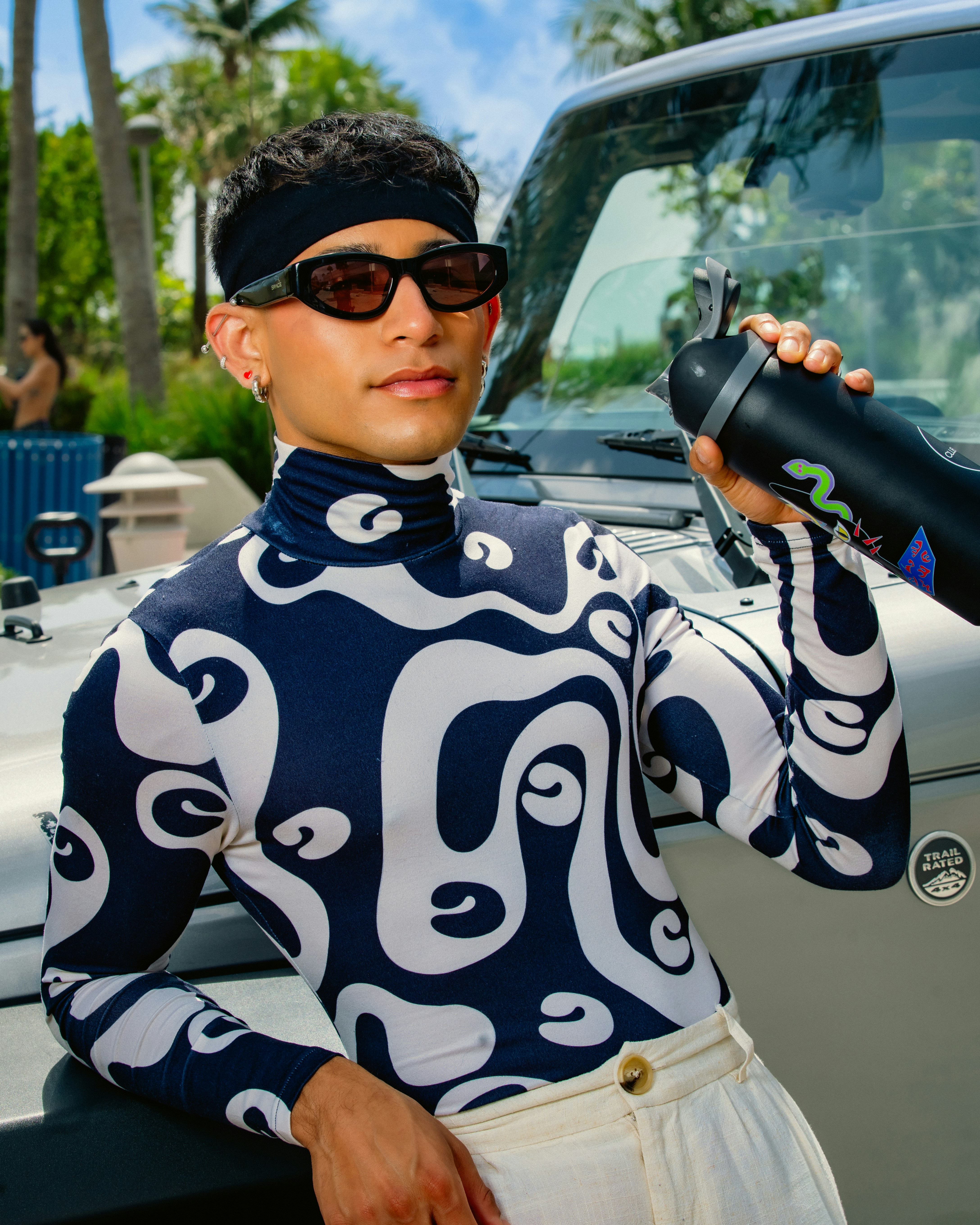 Man in patterned shirt holding water bottle near jeep.
