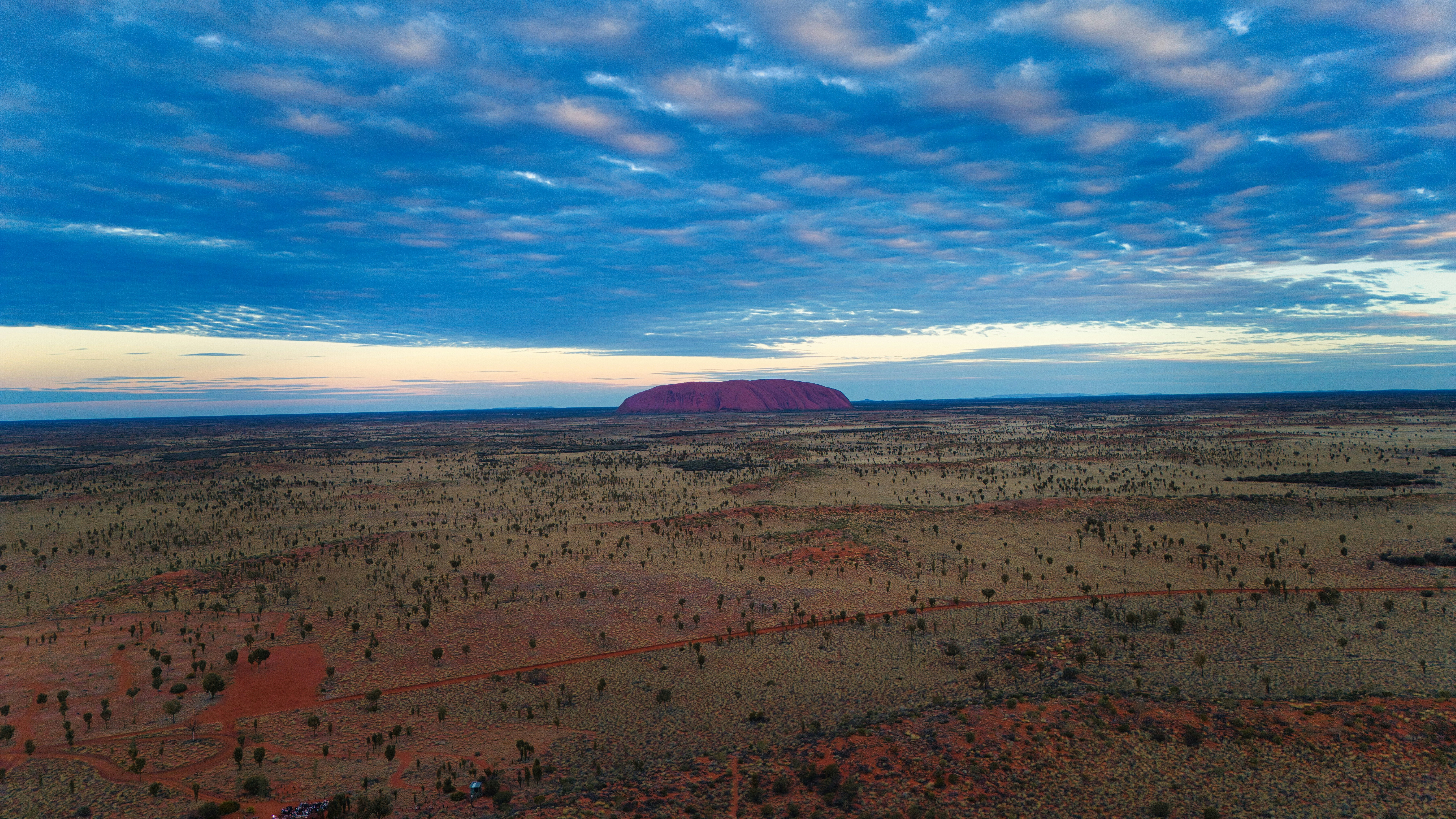 Vast desert landscape with Uluru rising majestically against a backdrop of colorful twilight skies.
