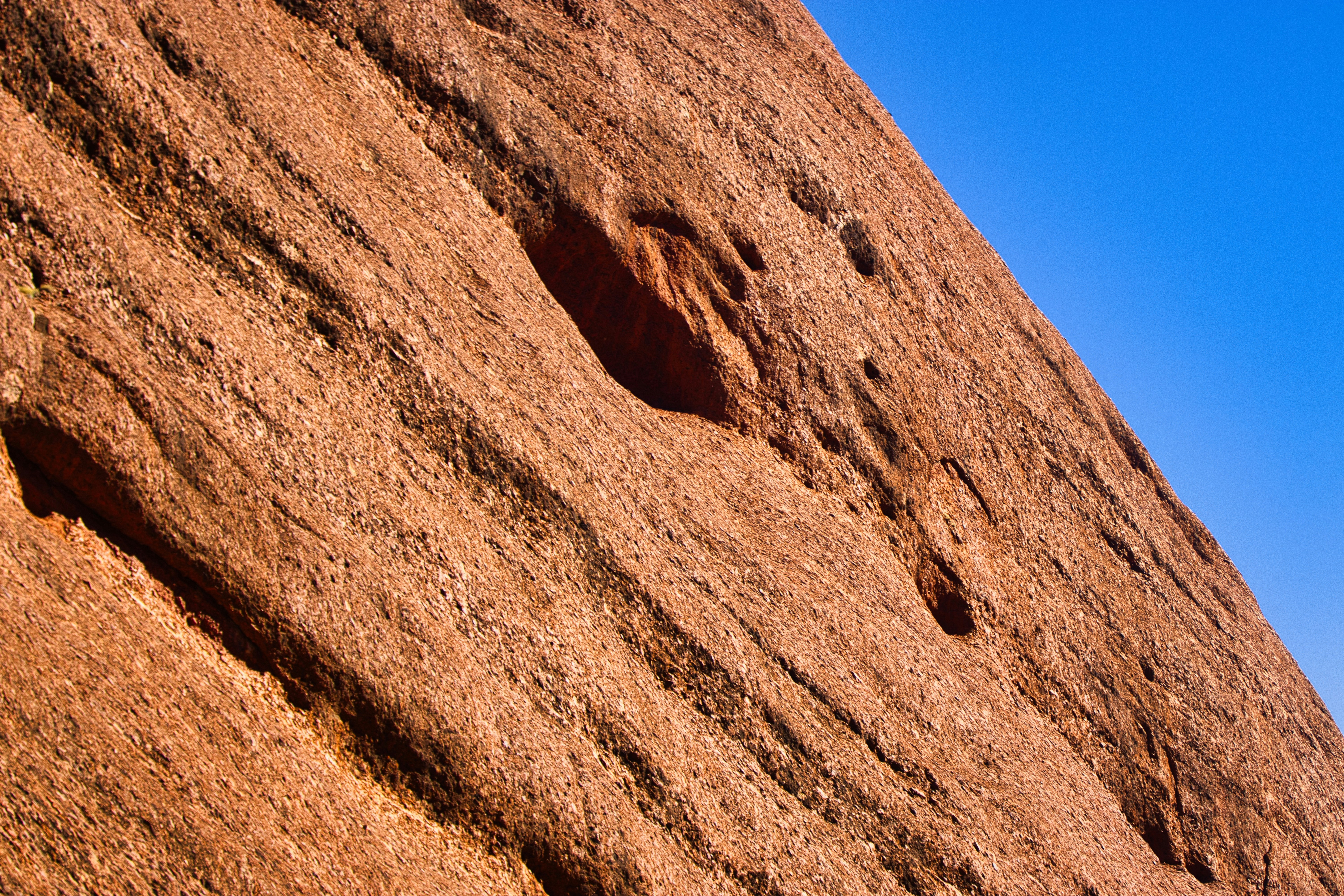 Crimson Cliff Contour: A Dark Hollow Carved into Stone Against an Azure Sky