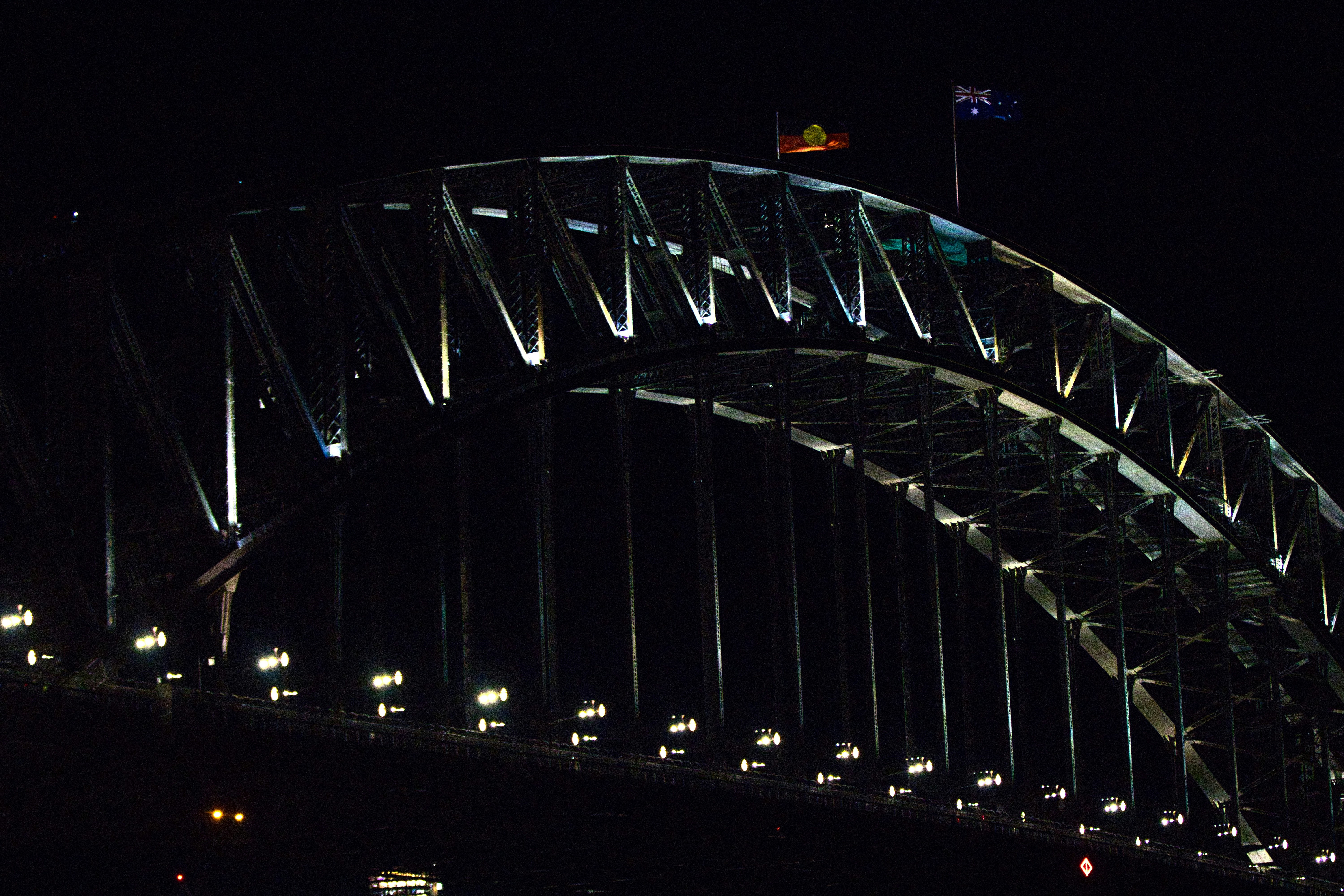 Sydney Harbour Bridge illuminated against the night sky, showcasing its architectural grandeur and the fluttering flags above.