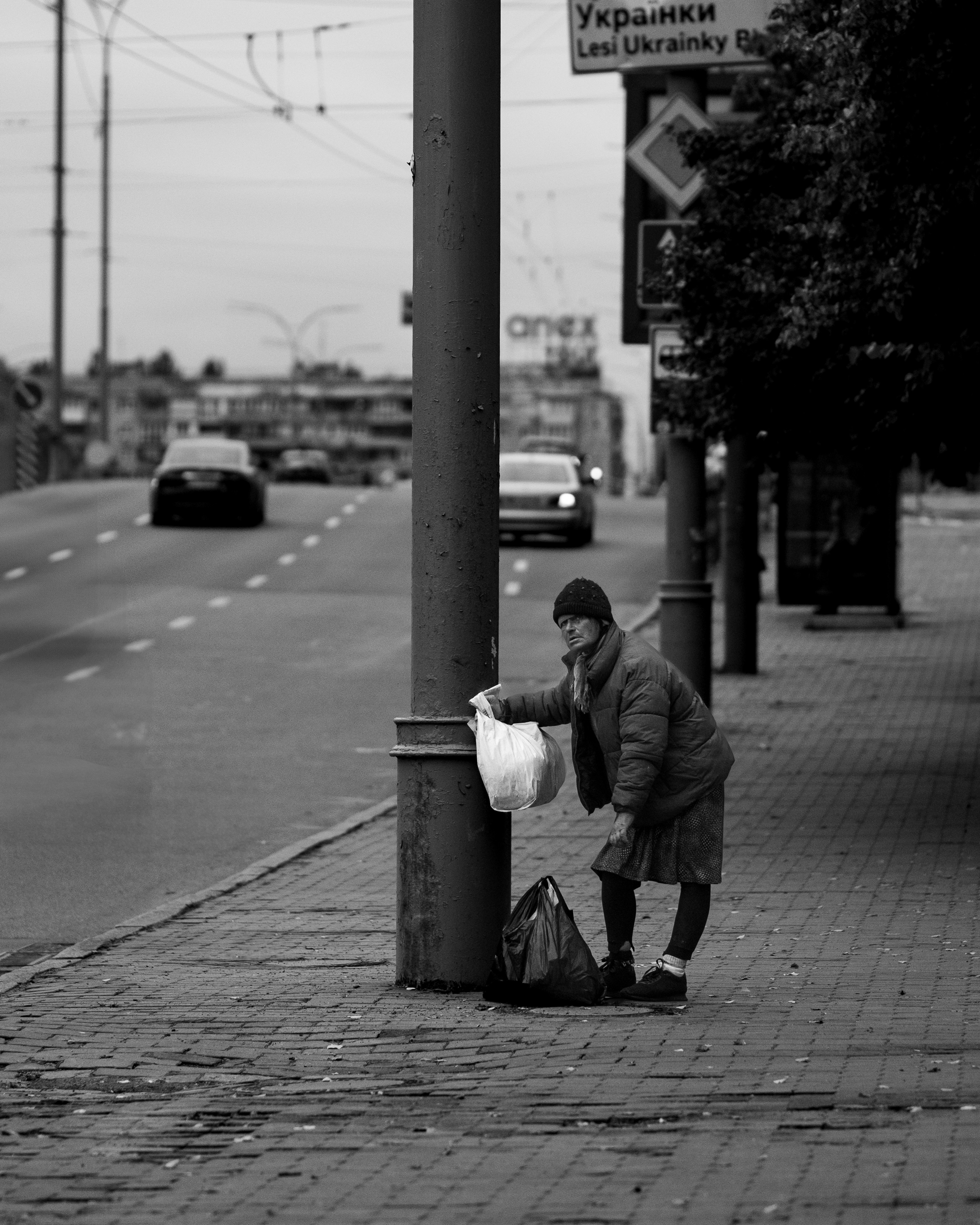 Elderly person collecting items by a street pole.