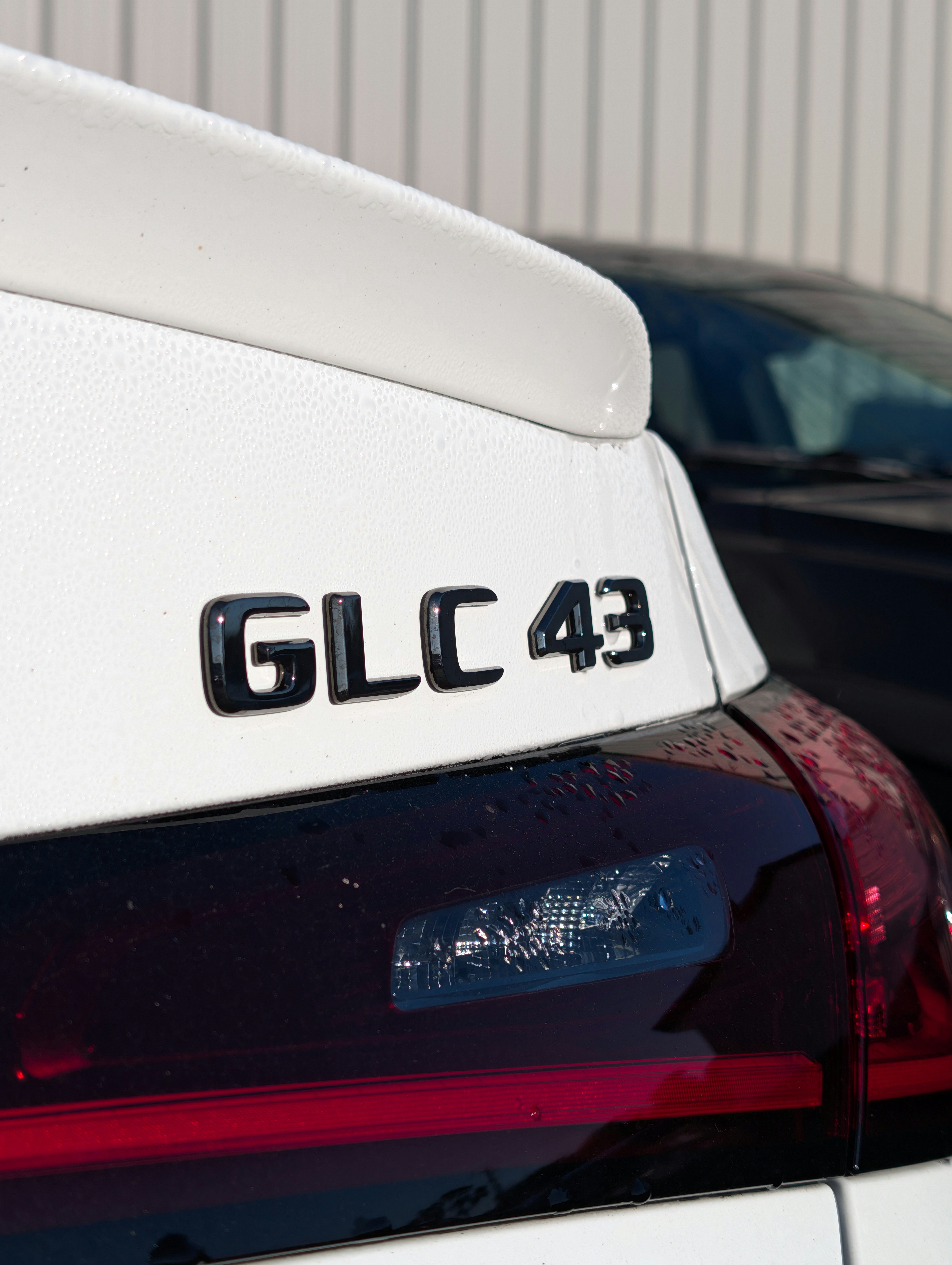 A perfect shot of the details that matter. The clean, black badging against the crisp white paint is a subtle yet powerful declaration of the incredible performance this AMG possesses. | Close-up of a white car's glc 43 emblem