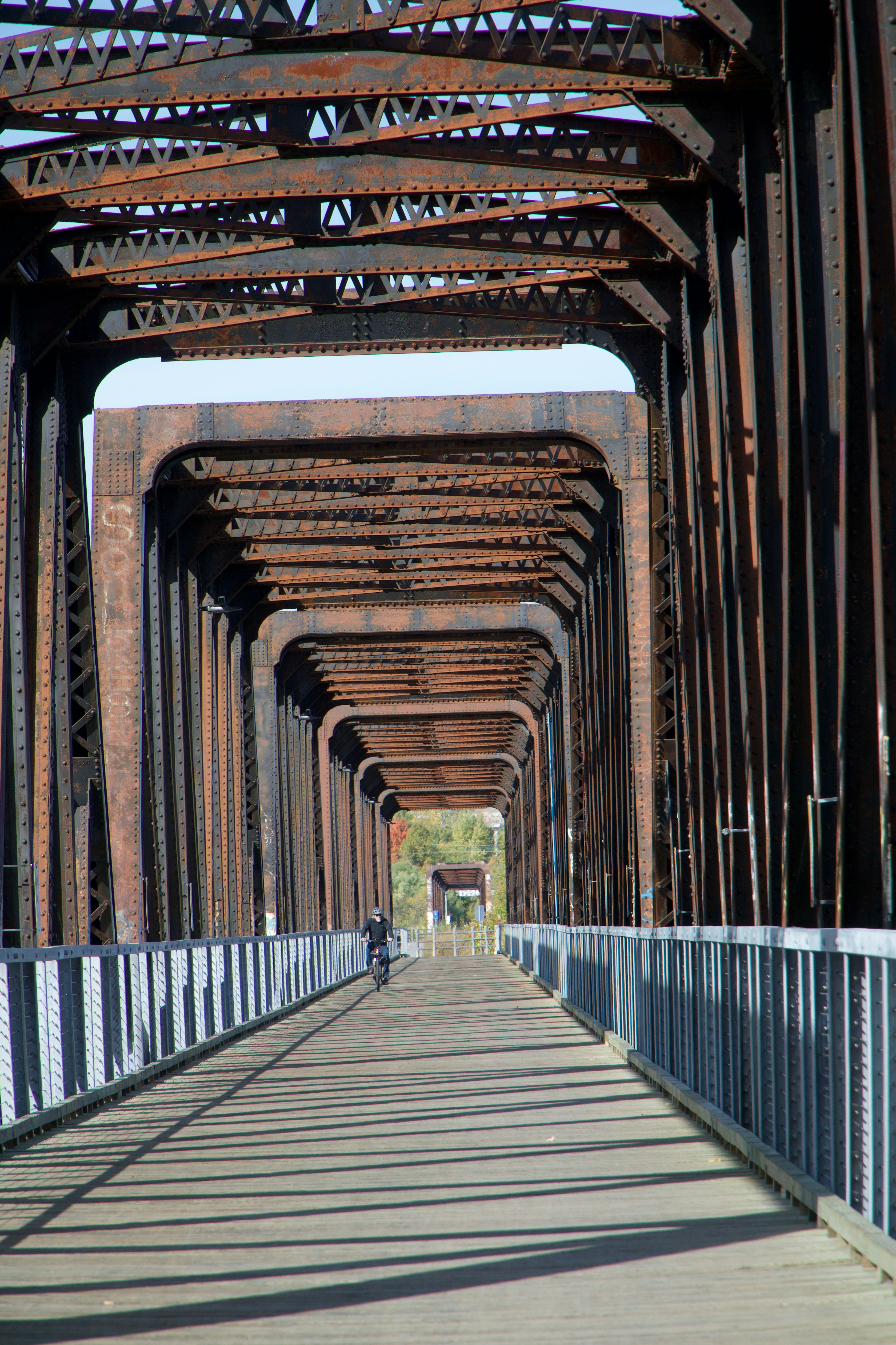 Chief William Commanda Bridge, converted to pedestrian and cycling uses | Perspective view of a rustic metal truss bridge walkway.