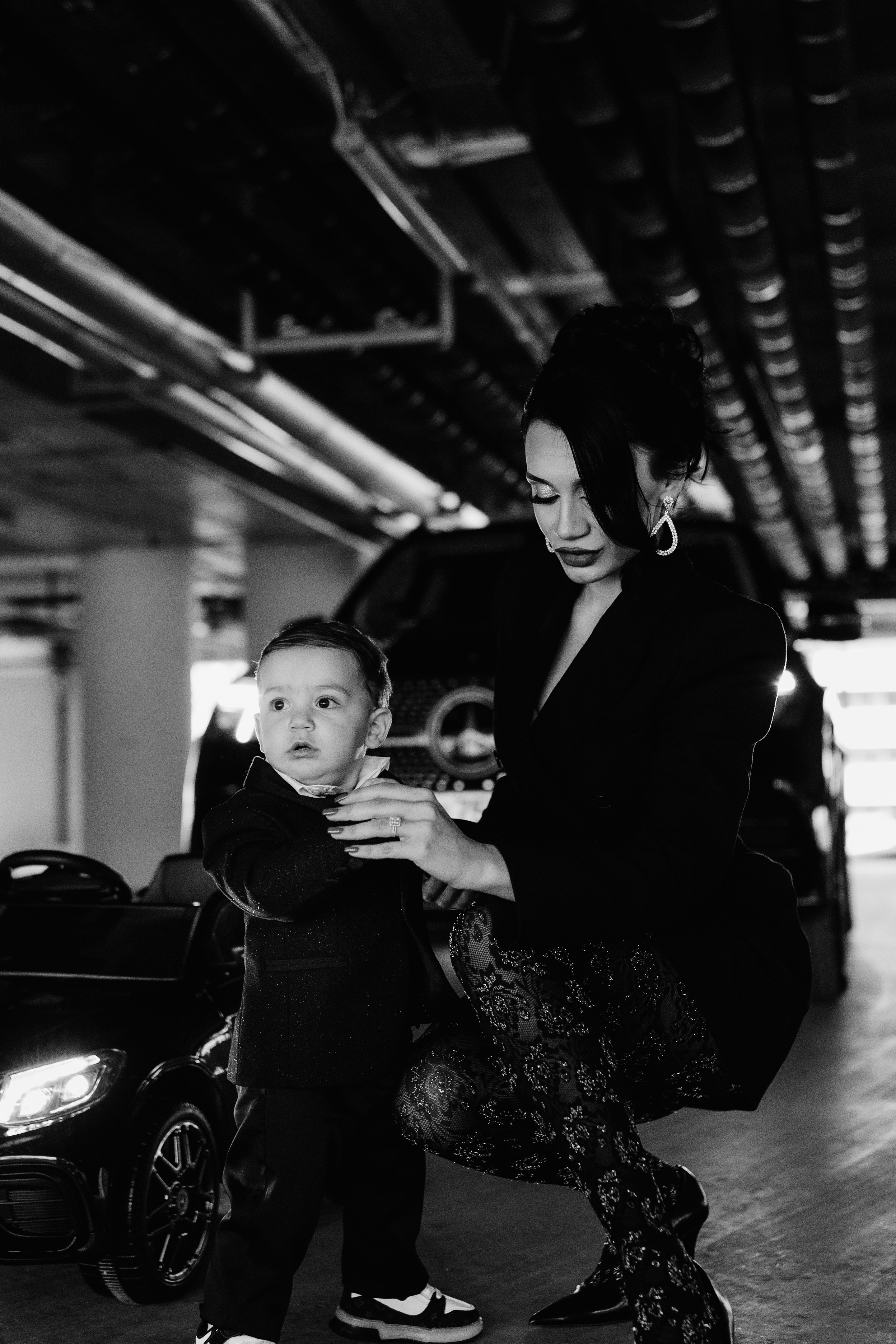 Monochrome Moment: A Mother and Baby Share a Quiet Moment beside a Toy Car in a Dim Parking Garage