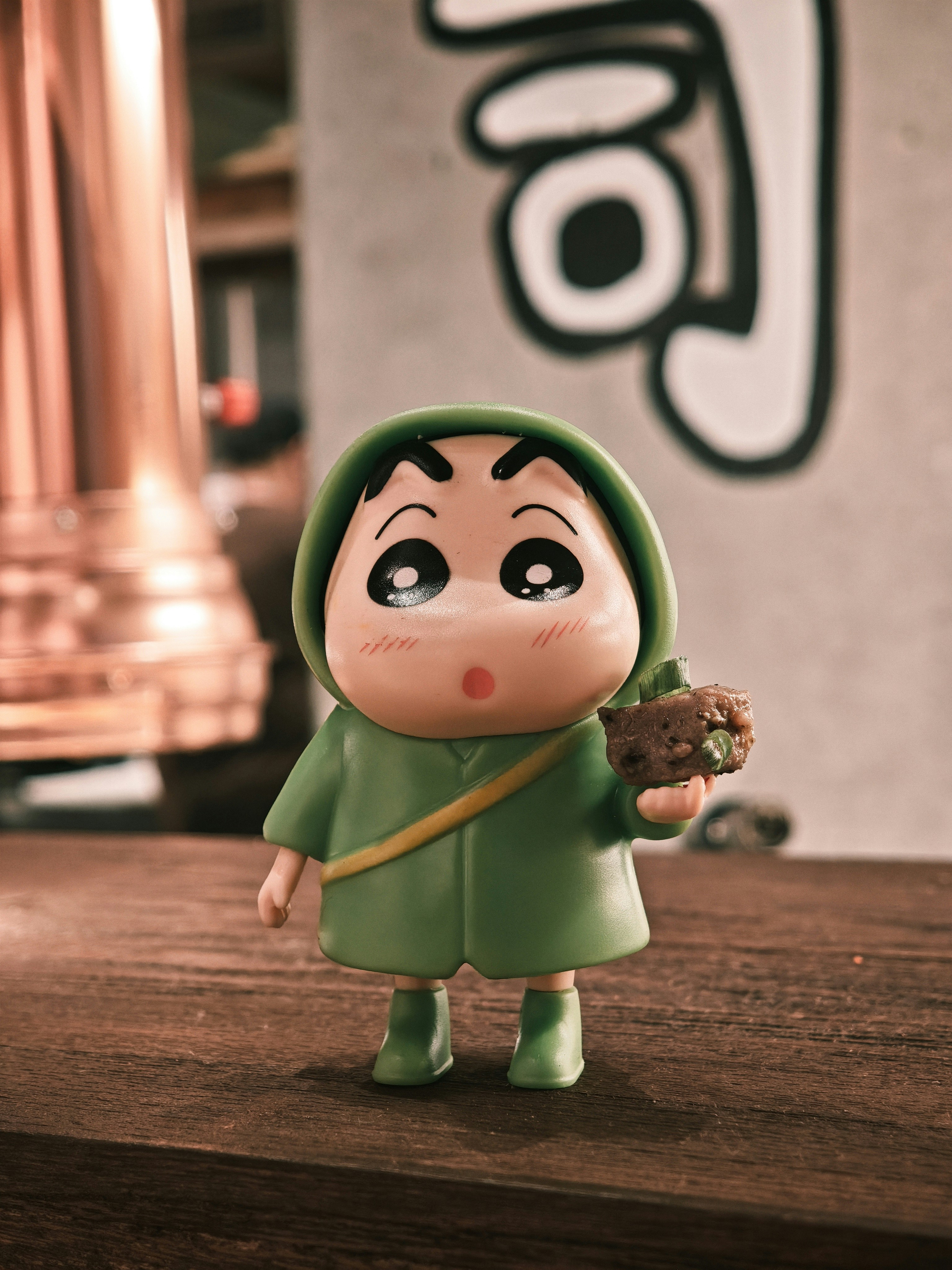 A cheerful green cartoon character holding a treat, set against a blurred background. The character's expressive eyes and vibrant colors evoke a sense of joy.