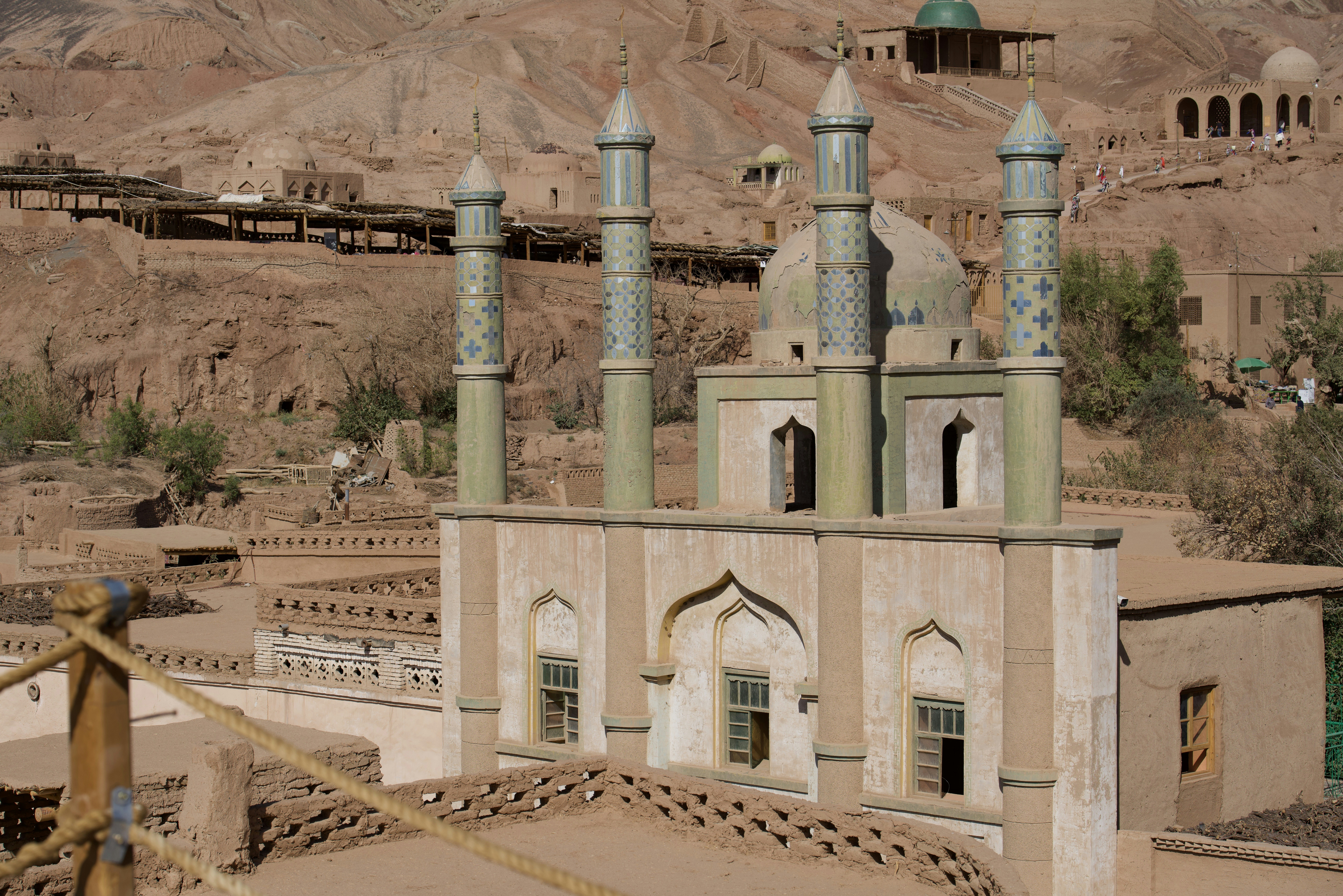 Historic mosque with colorful minarets surrounded by earthen structures in a desert landscape.