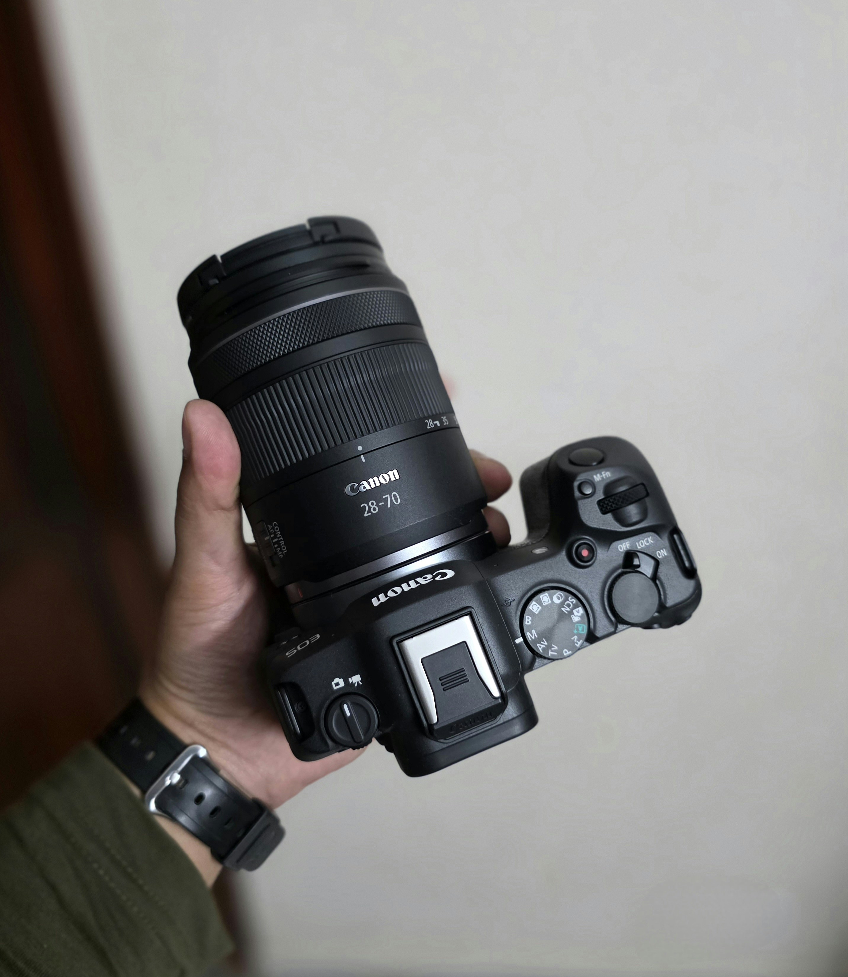 A hand holds a black canon camera with lens.