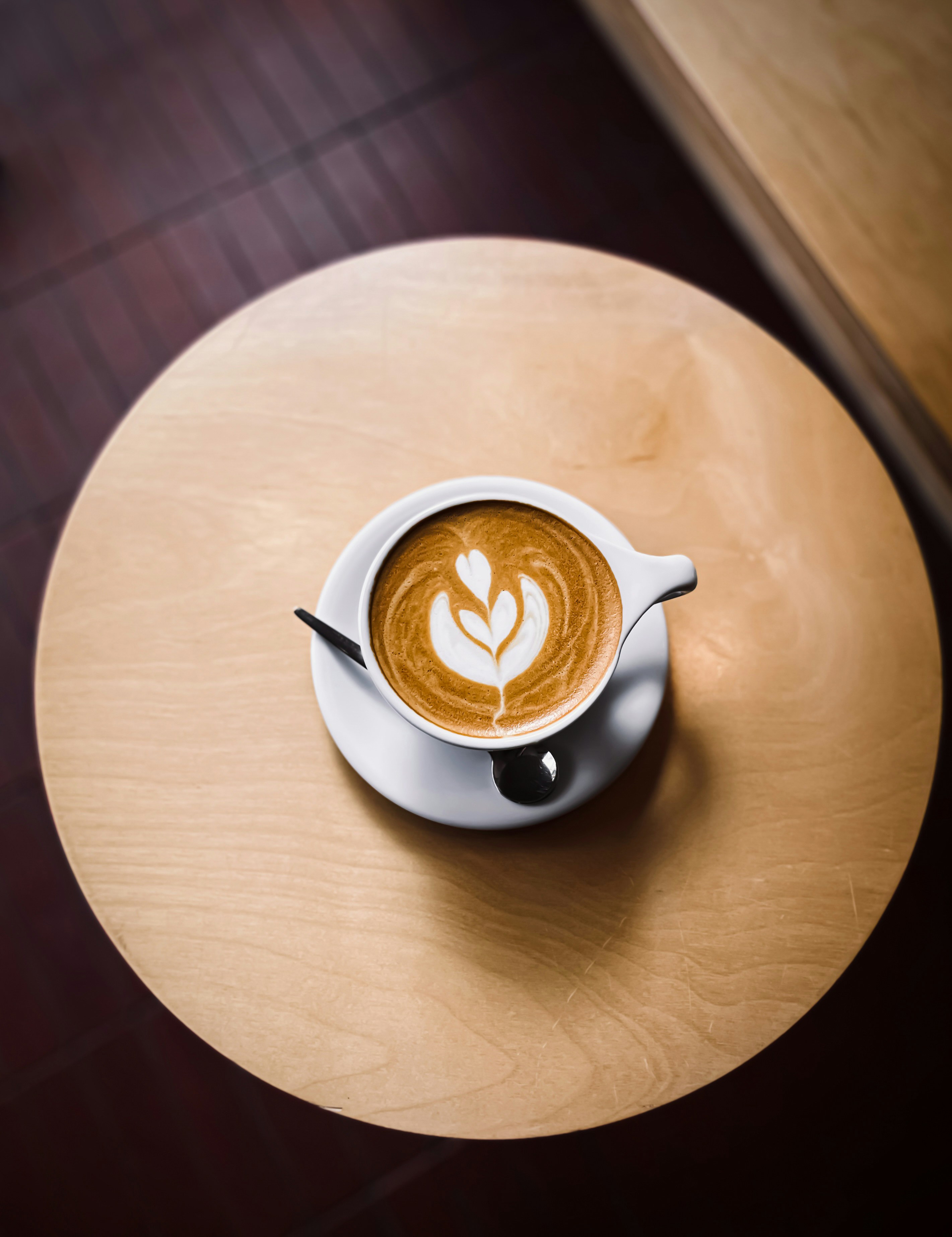 Latte art displayed in a white cup on a wooden table, showcasing intricate designs atop the coffee surface.
