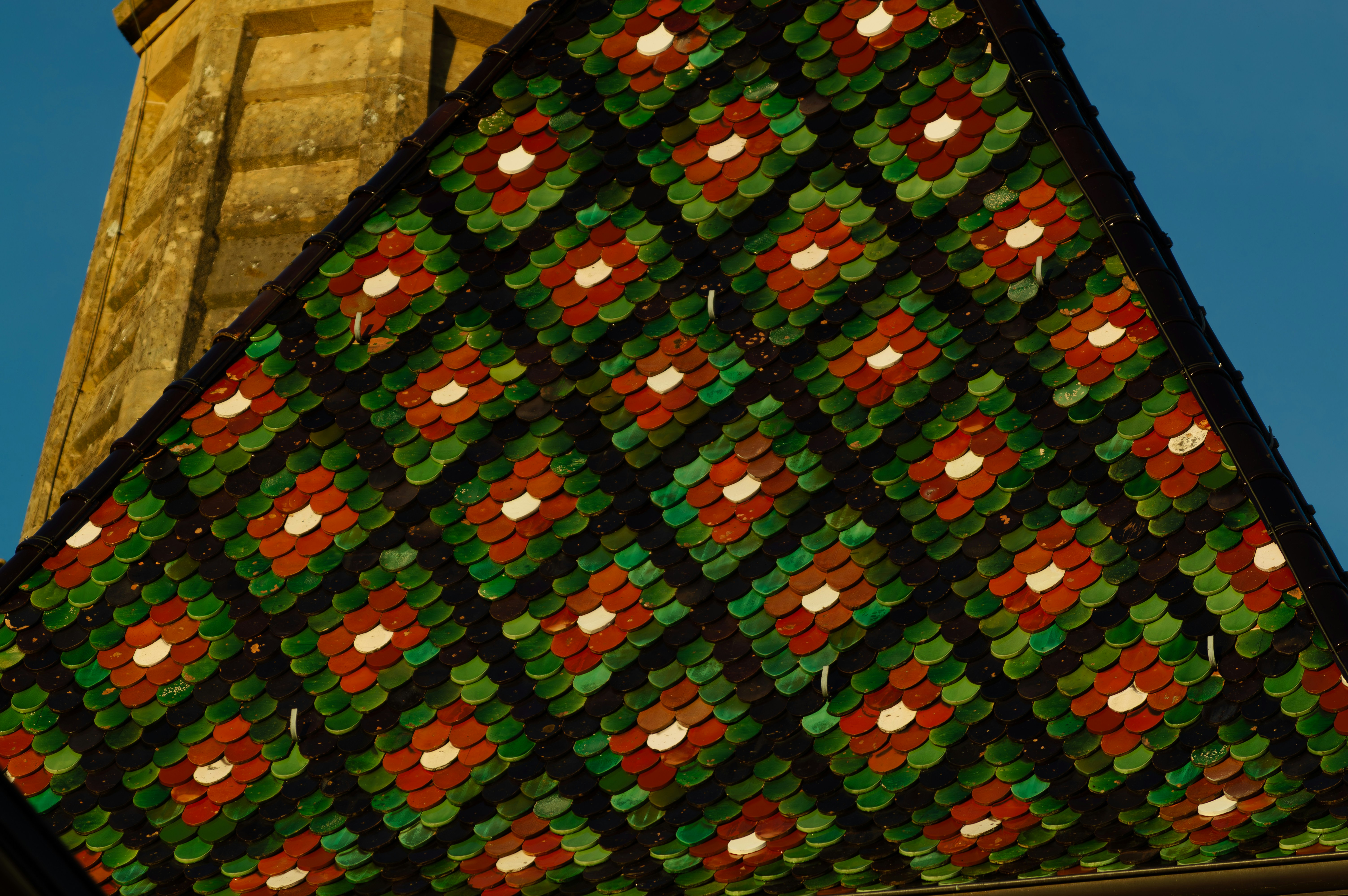 Intricate tiled roof featuring a vibrant pattern of red, green, and white tiles against a clear blue sky.
