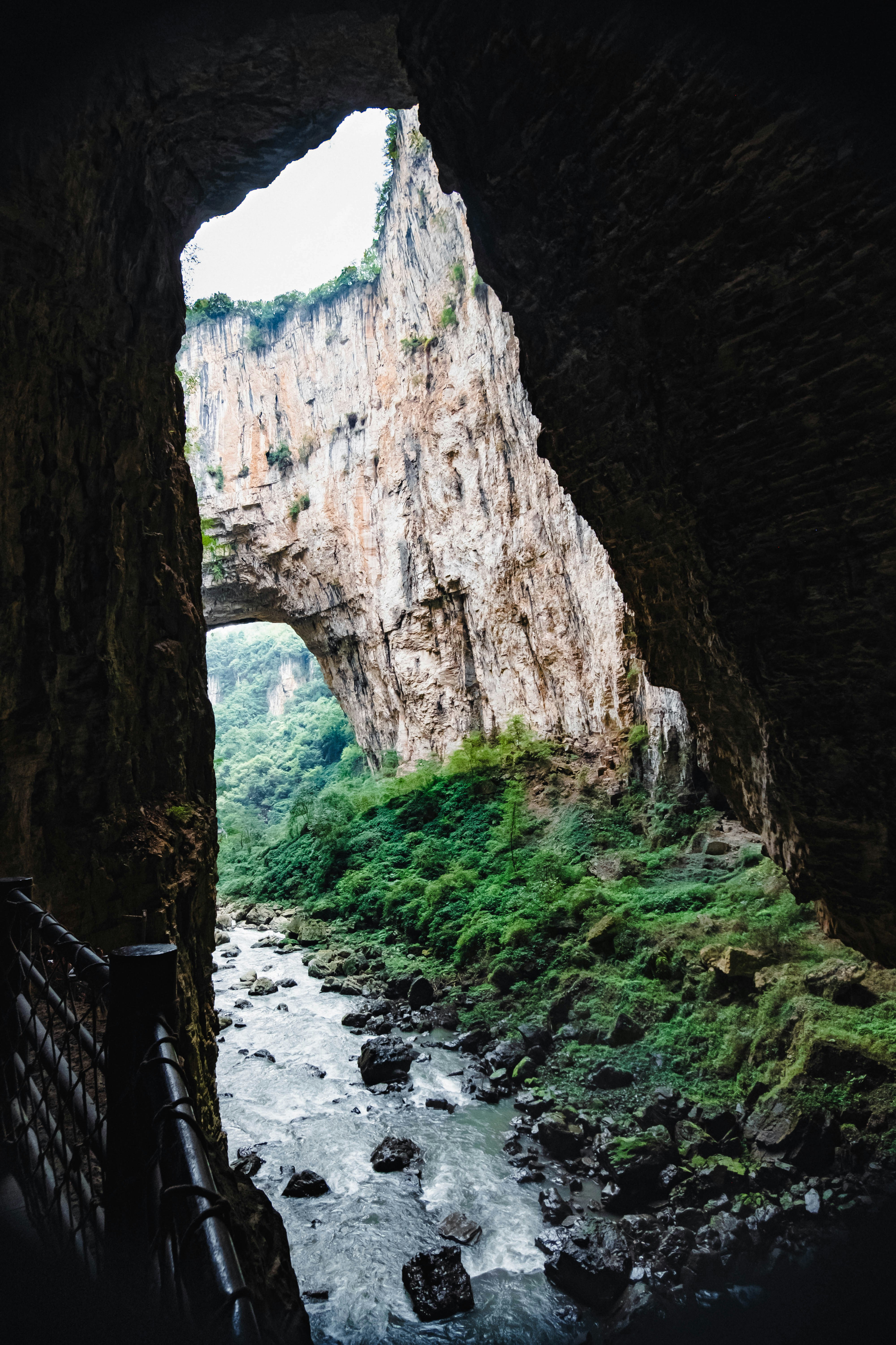 A breathtaking view through a natural stone arch, revealing a lush river valley below. The rugged cliffs frame the serene waterway and dense greenery.