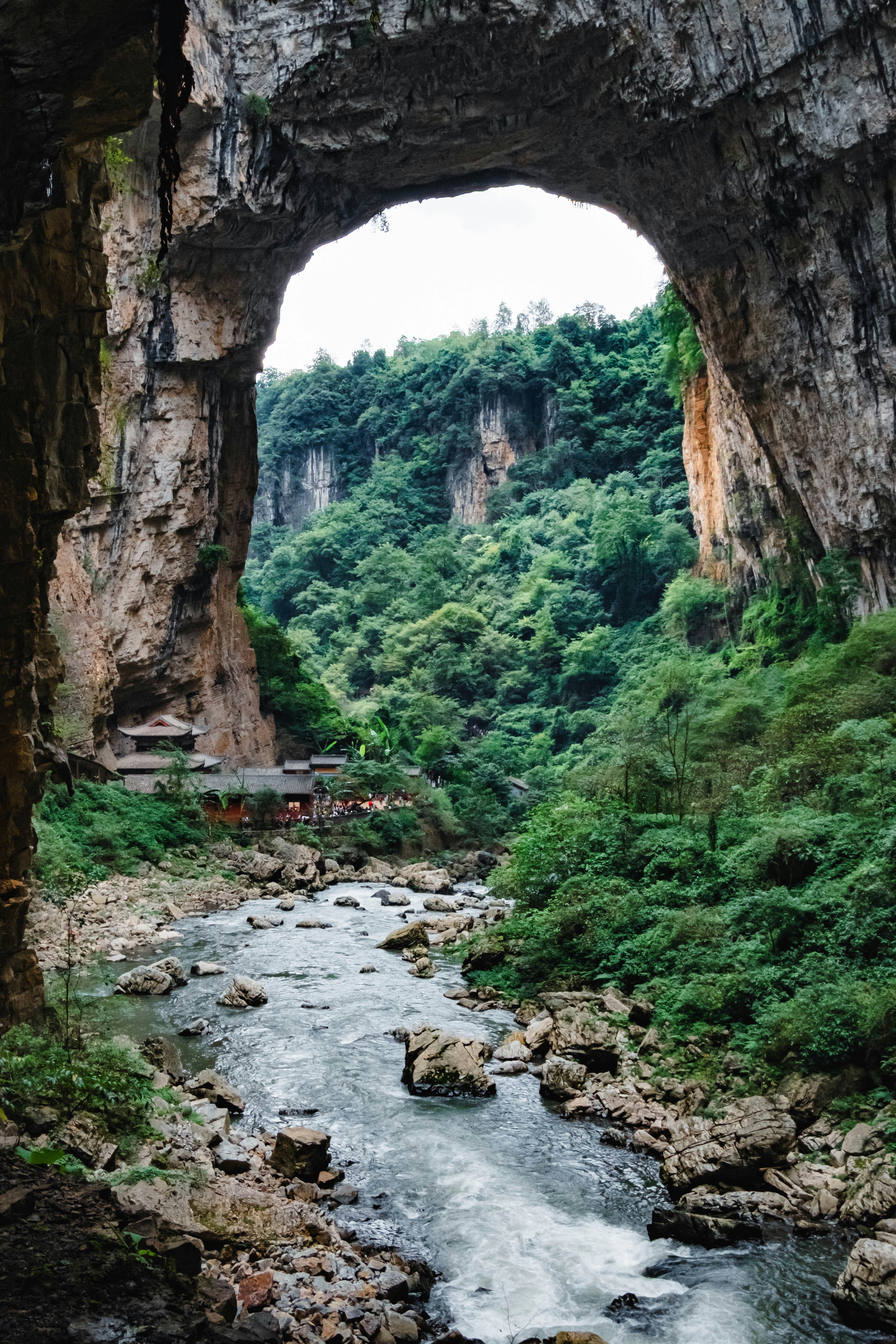 Natural rock arch over a lush green valley and river.