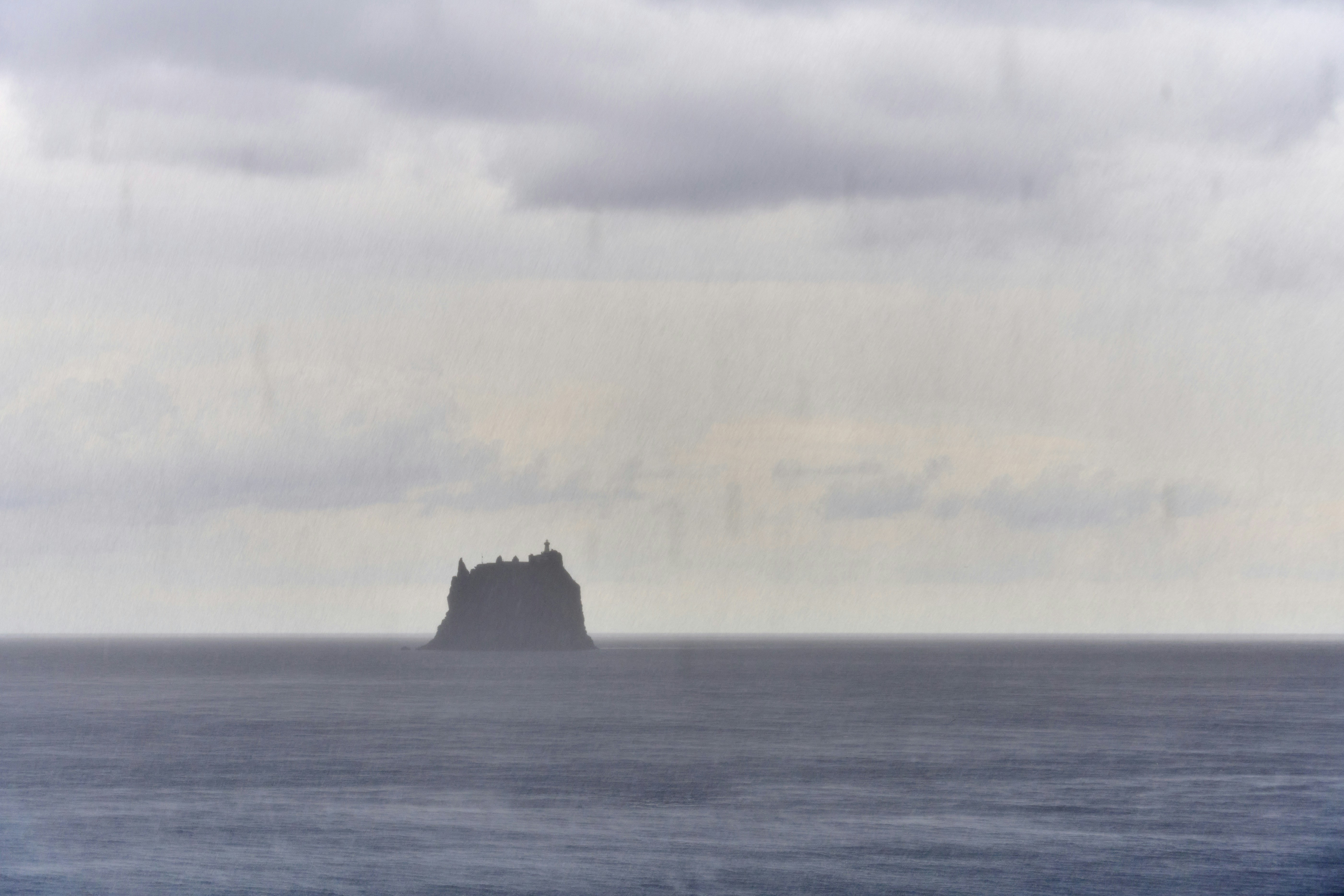A remote island rises from the ocean, shrouded in mist and mystery, under an overcast sky.