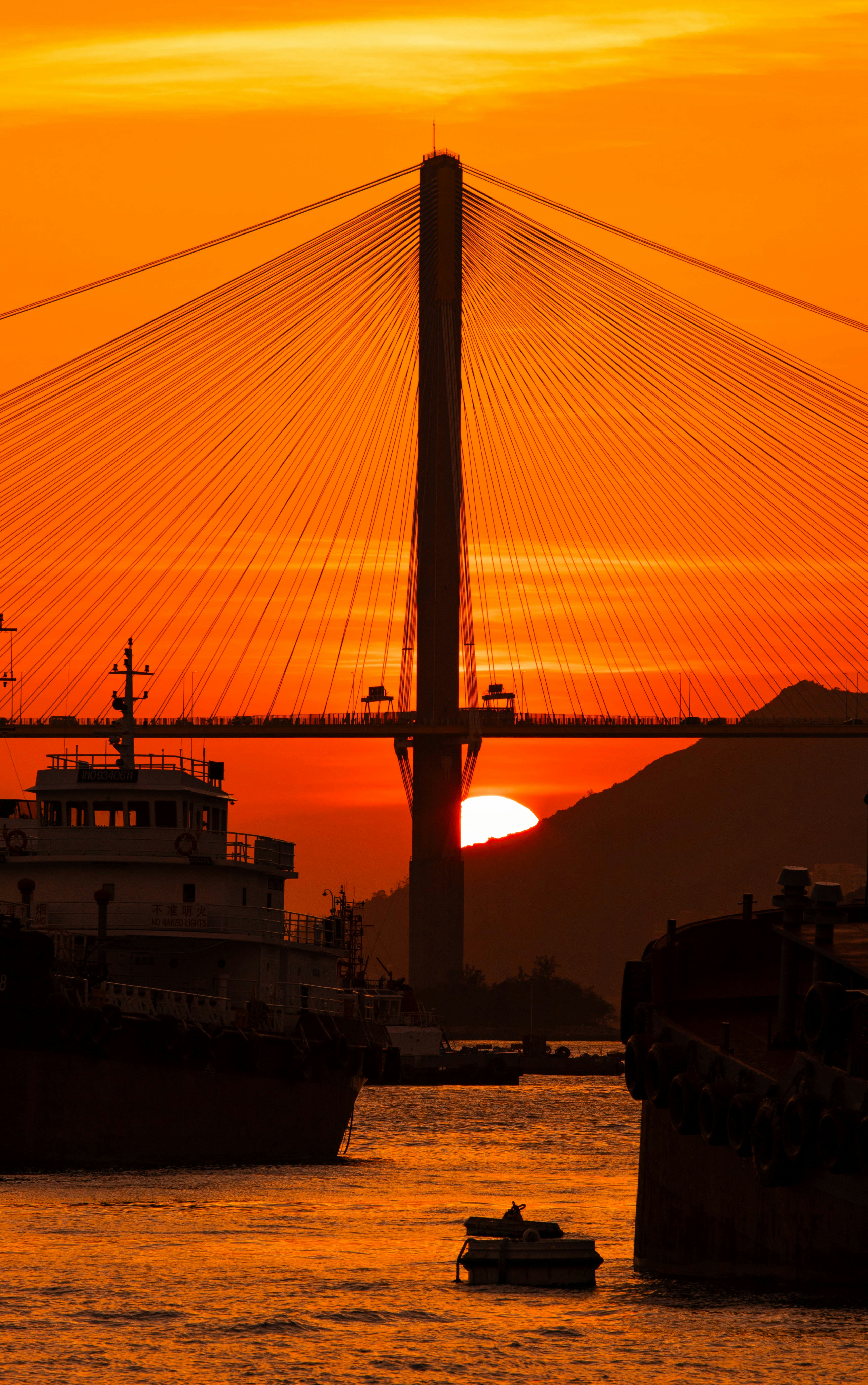 Ships and bridge silhouetted against a vibrant sunset.