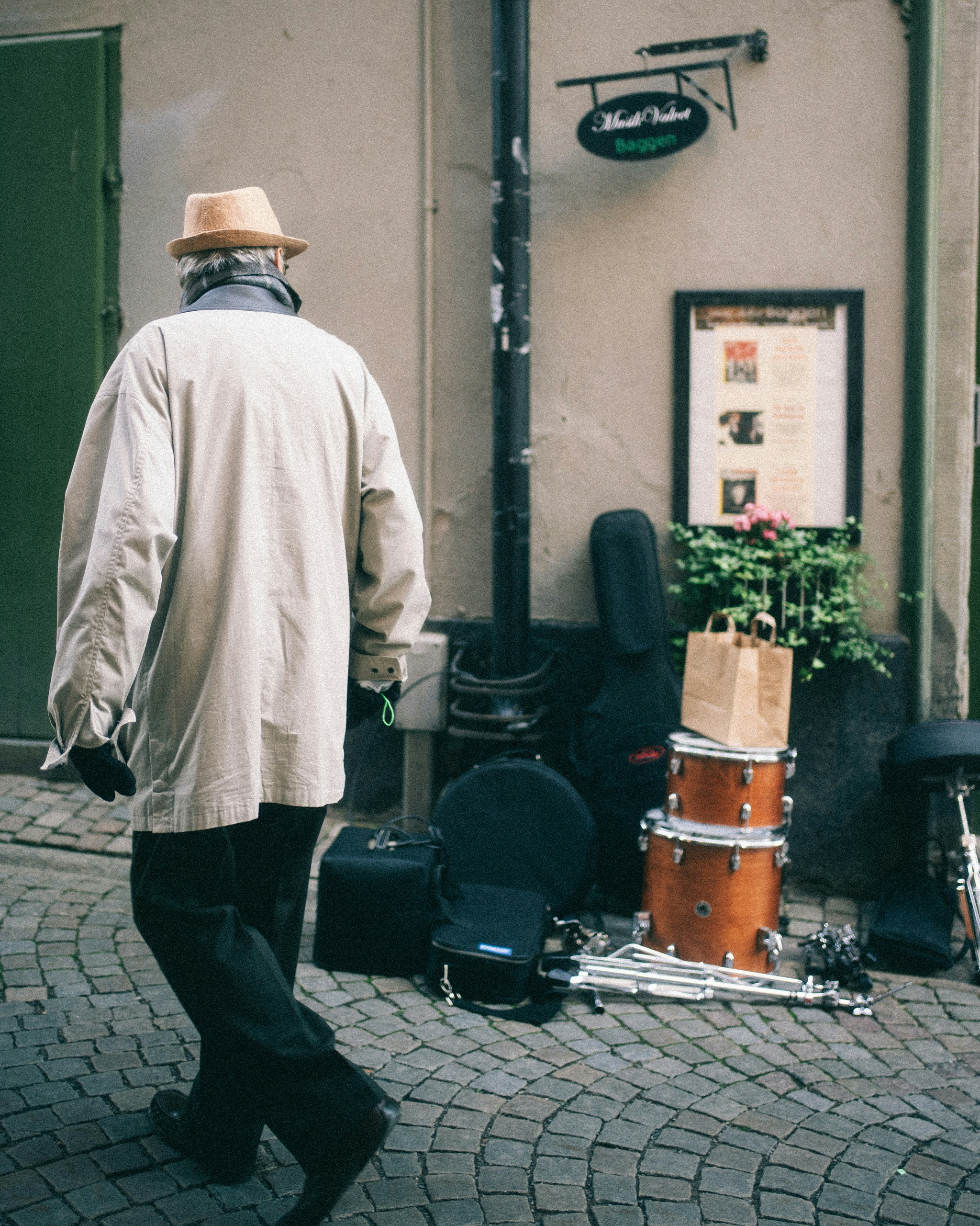 Instagram: @withdanial | Man in hat walks past drums on cobblestone street