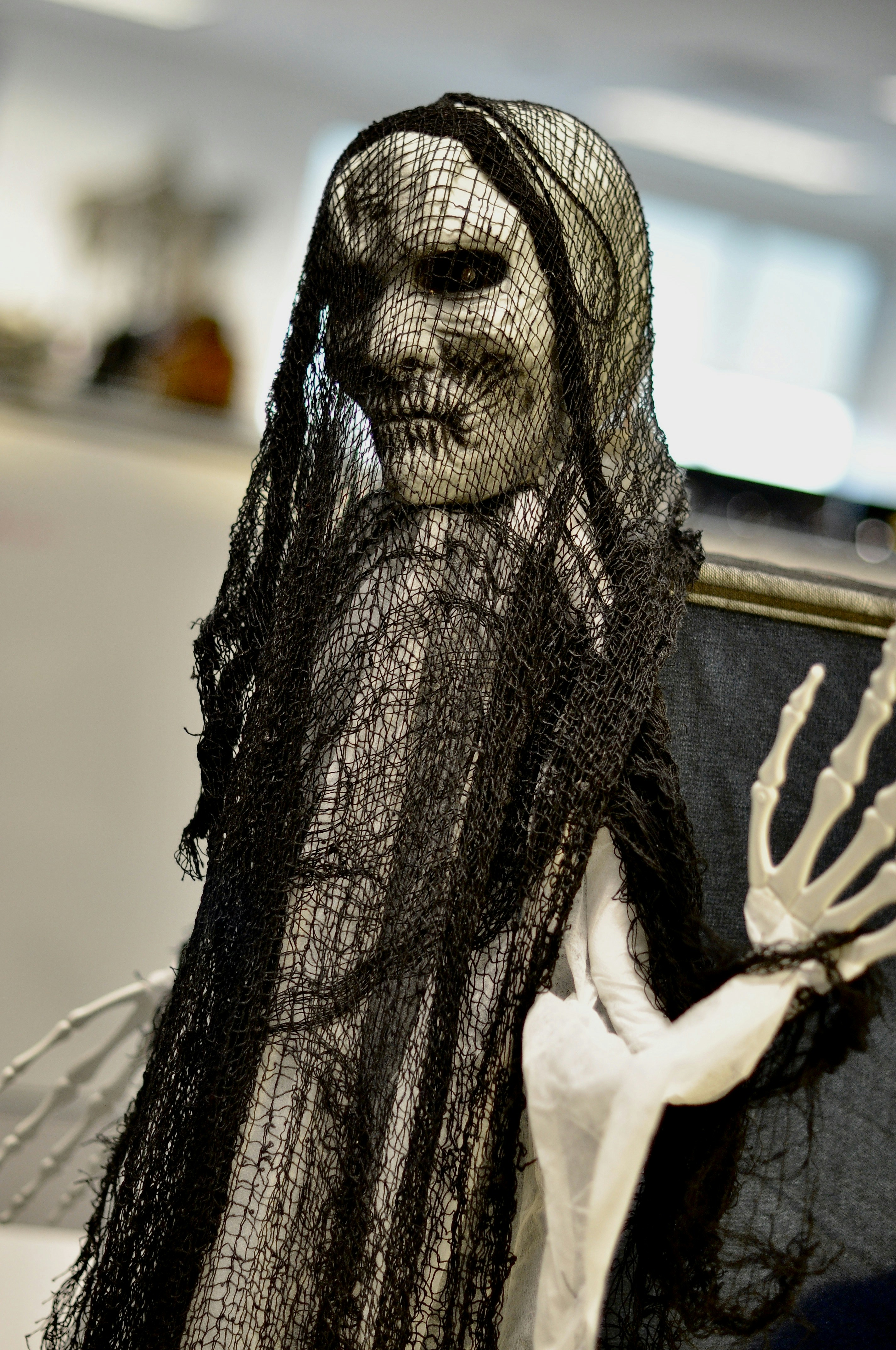 A ghostly figure draped in dark fabric, with skeletal hands peeking through, evokes an eerie atmosphere in a dimly lit space.