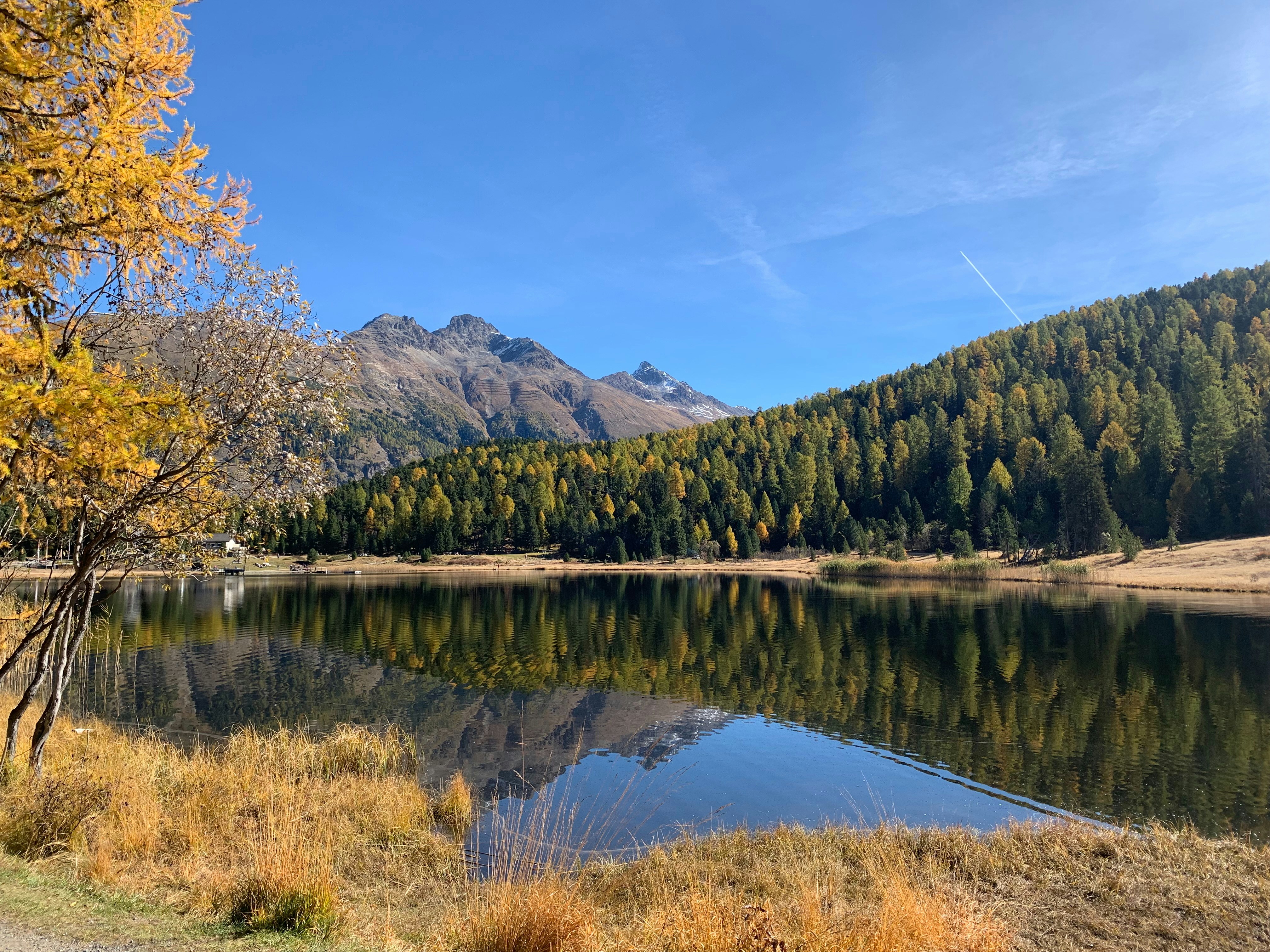 Vibrant autumn foliage surrounds a tranquil lake, with majestic mountains reflecting in the still water. The scene captures the essence of nature's transition.