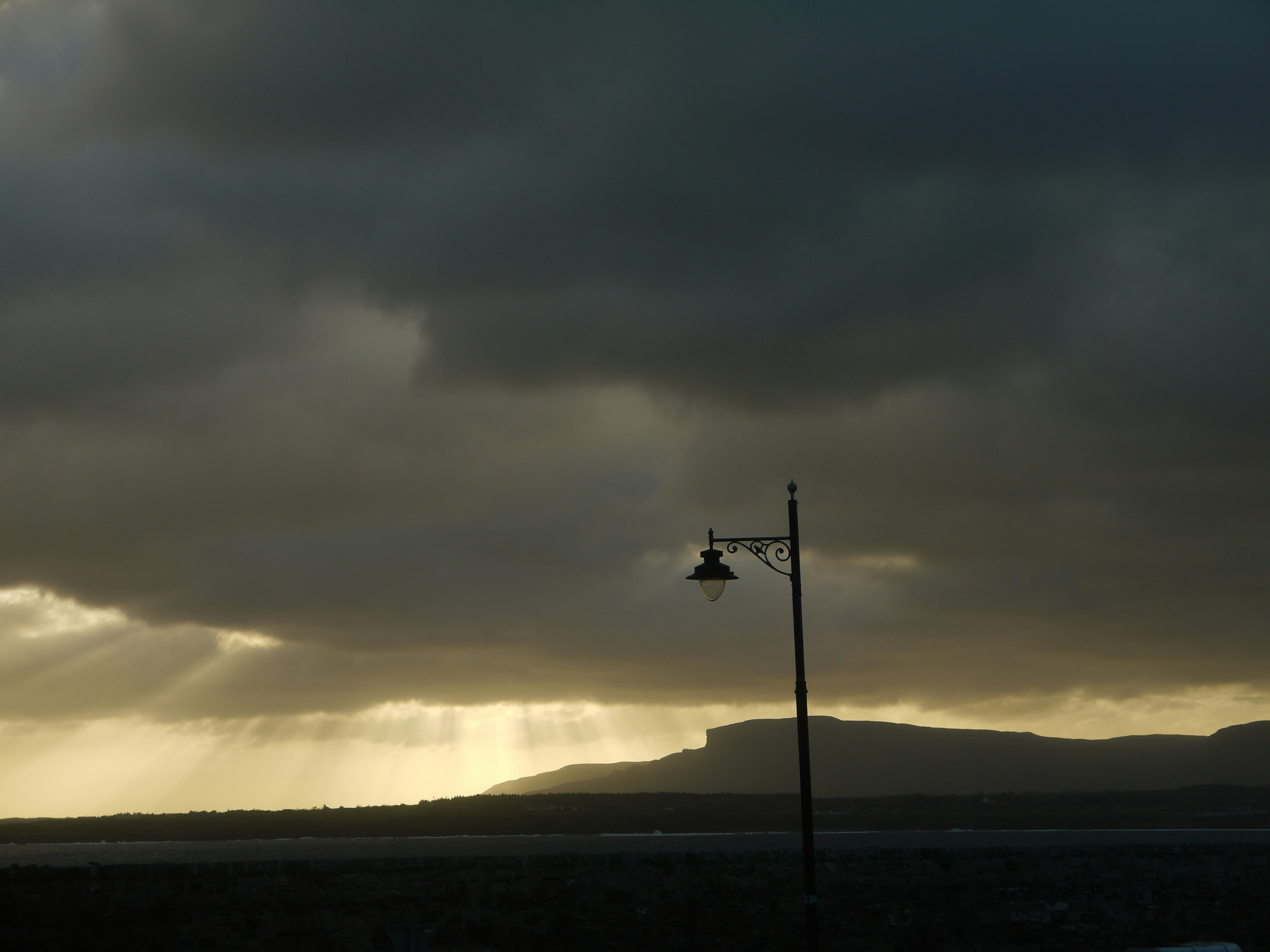 Lone Lamp at Sunset: Sunbeams Break Through a Brooding Horizon