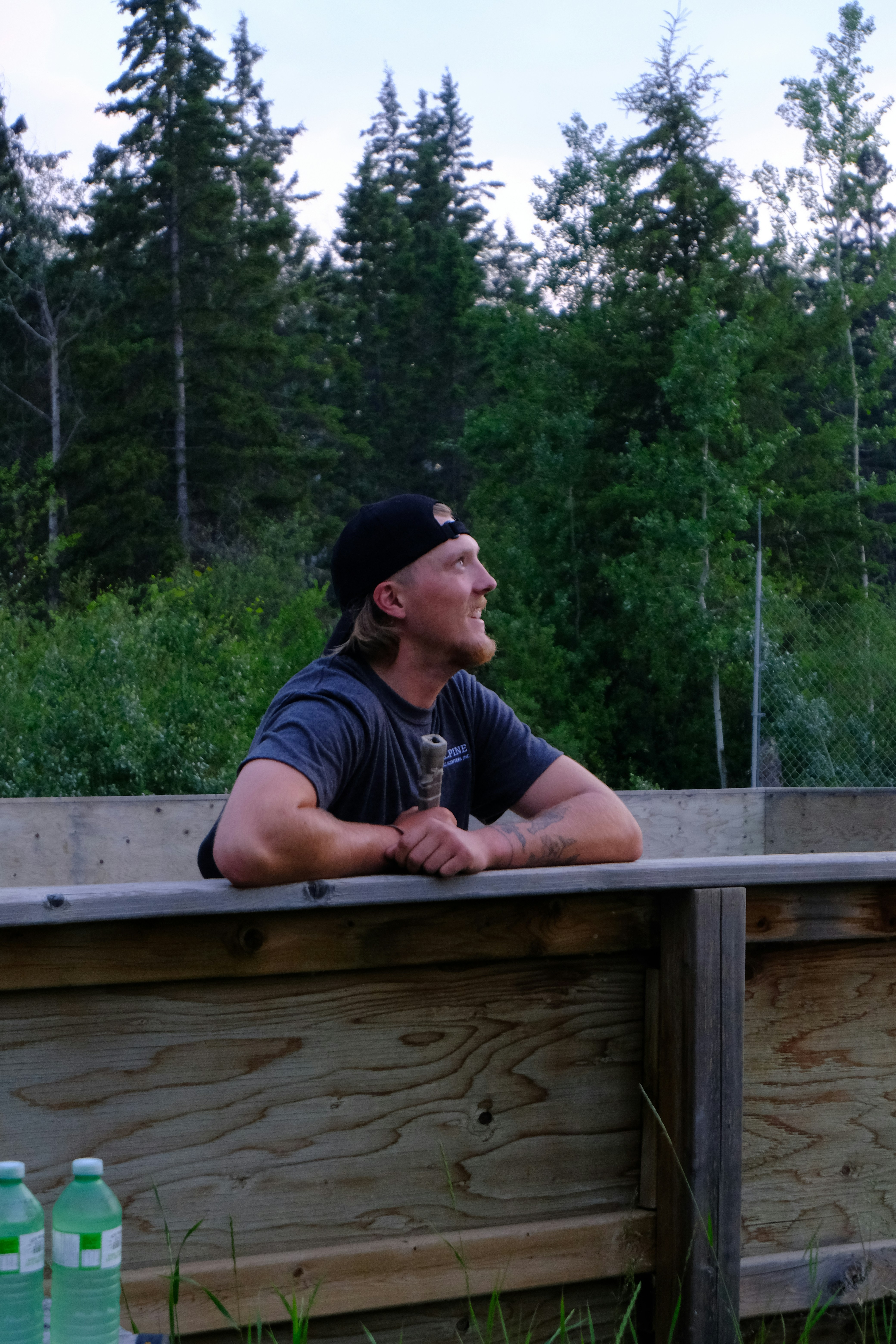 Man in a baseball cap leans on a wooden railing.