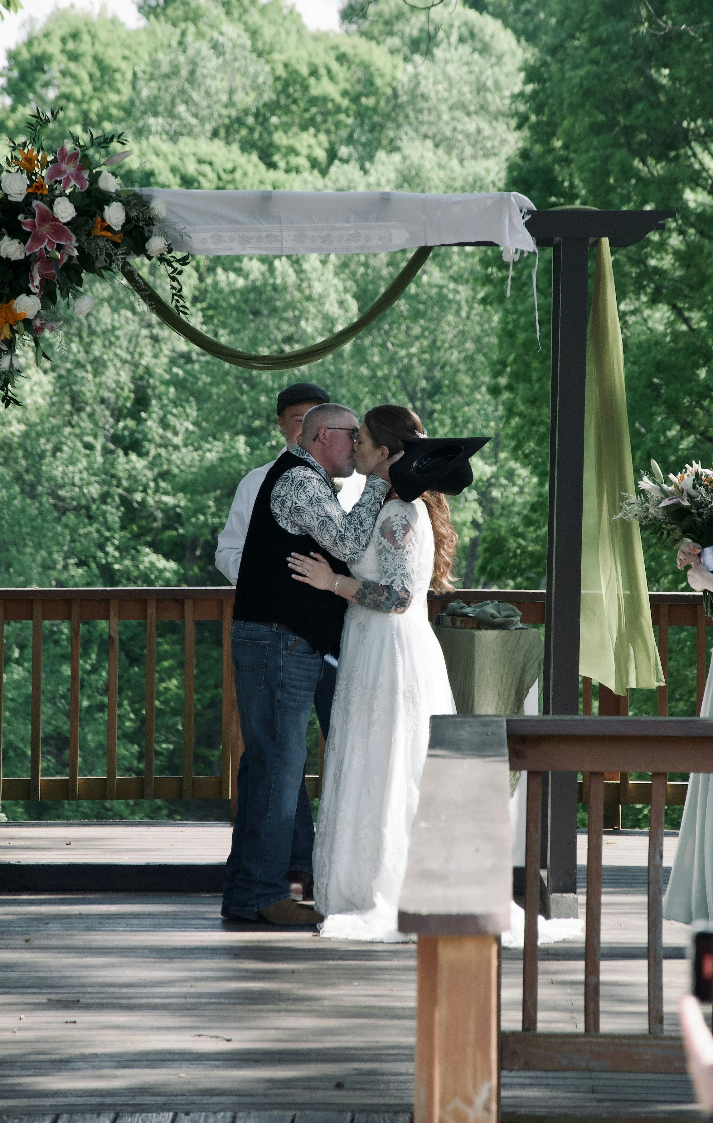 Couple sharing a kiss during their wedding ceremony under an adorned archway, surrounded by lush greenery.