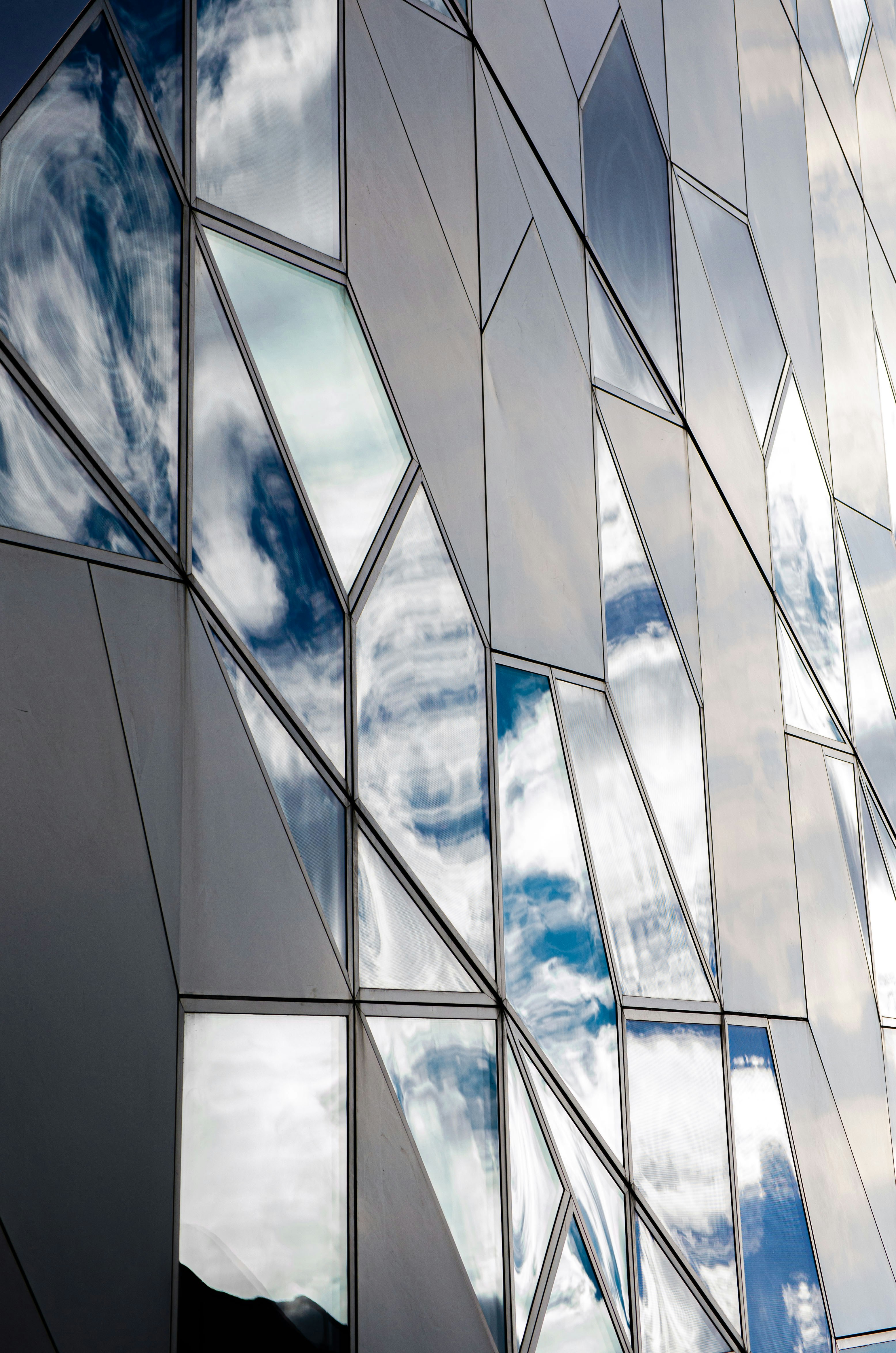 Geometric building facade reflecting clouds and sky, showcasing a dynamic interplay of light and form.