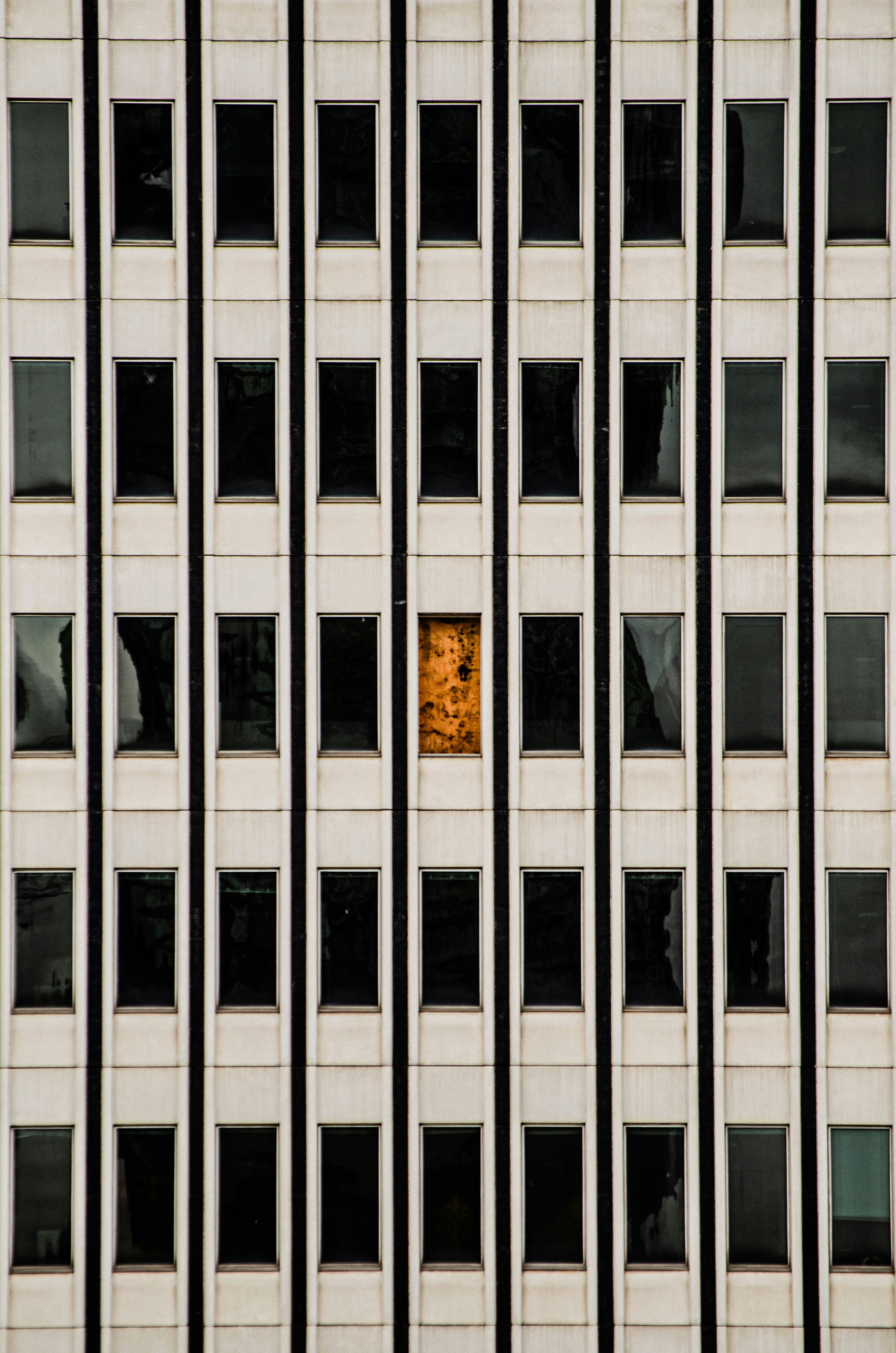 A solitary golden window stands out among a grid of darkened glass panels on a modern building facade.