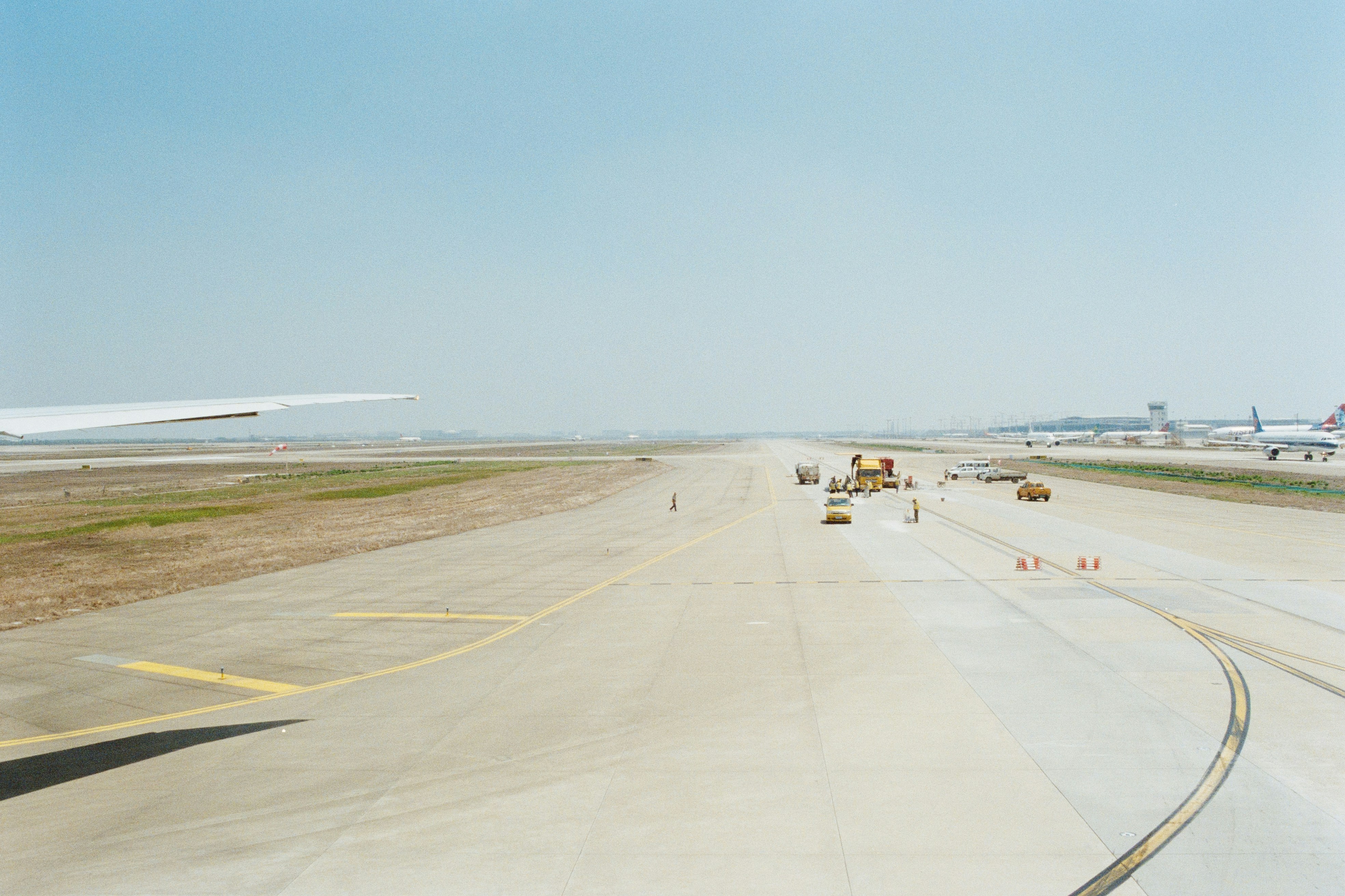 🎞️ Alien Film CN400 ProMax｜🧪 Fuji Hunt C-41｜🖨️ EOS R6 + RF 100mm f/2.8L Macro｜📷 Canon New F-1 + FD 35mm 1:2 S.S.C. | Airport runway with vehicles and distant planes
