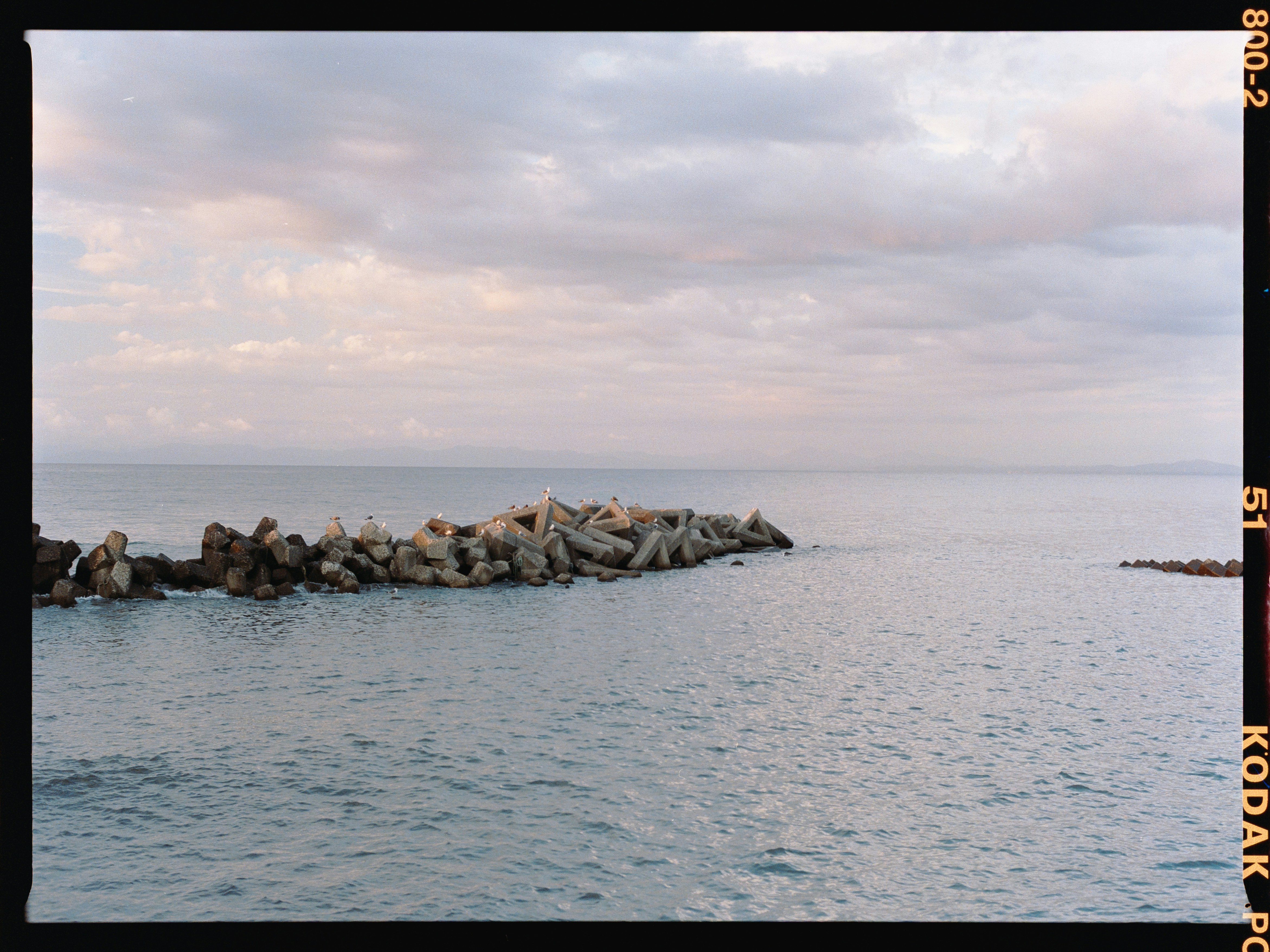 Rocky jetty extending into calm waters under a soft, cloudy sky.