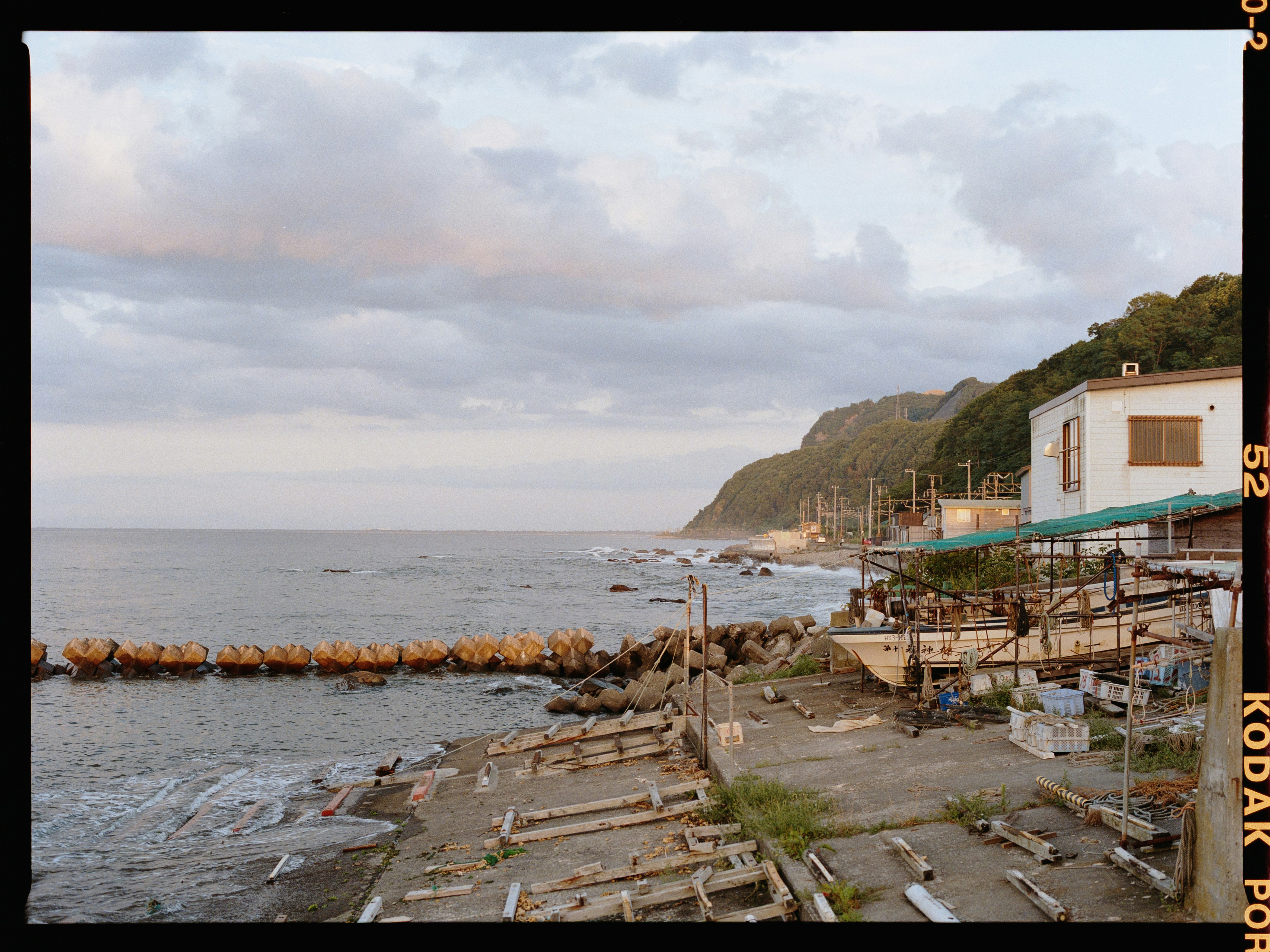 Fishing boats and rocky shoreline at dusk, with gentle waves lapping against the coast. The distant hills frame the serene landscape.