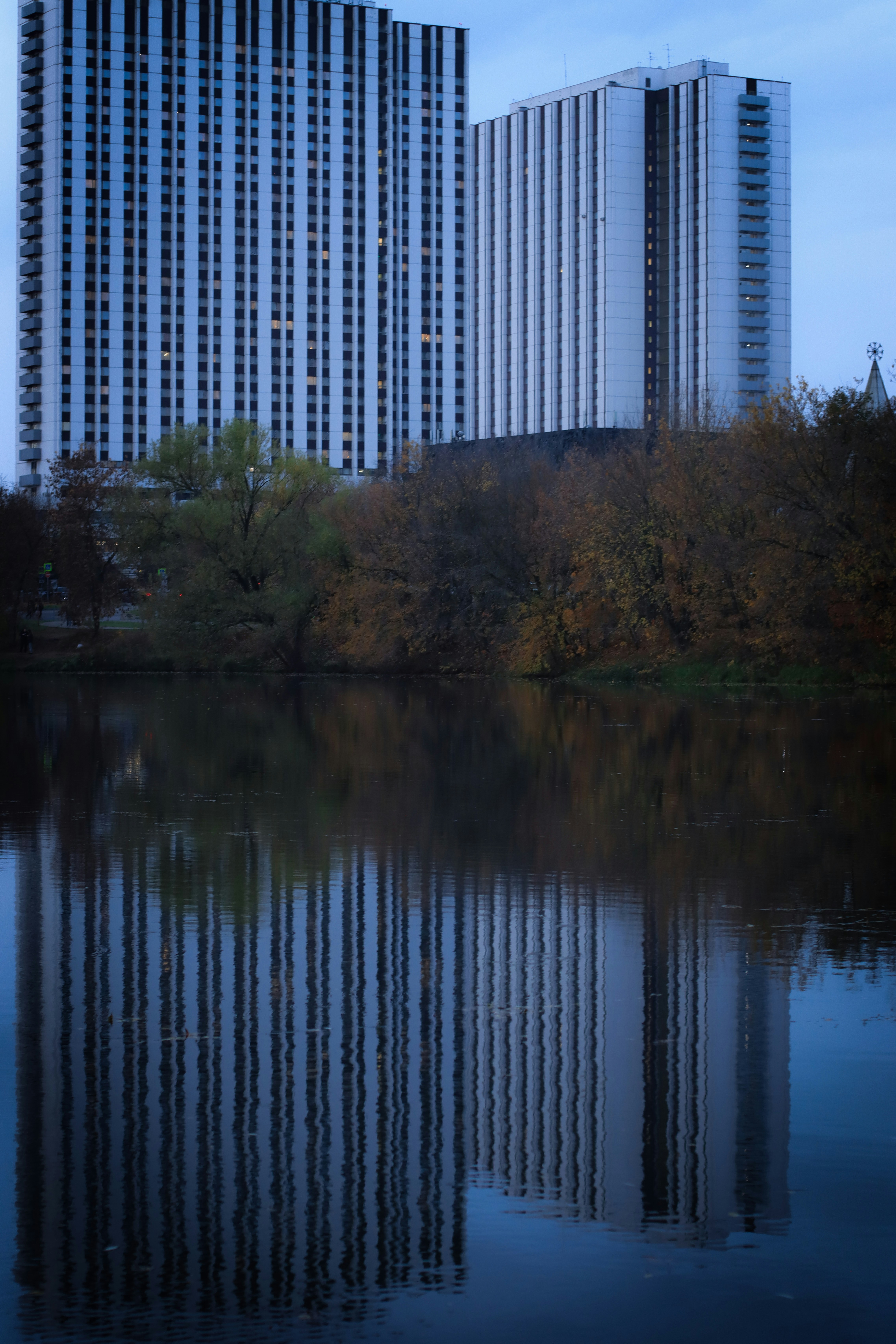 Two tall buildings reflected in calm water.