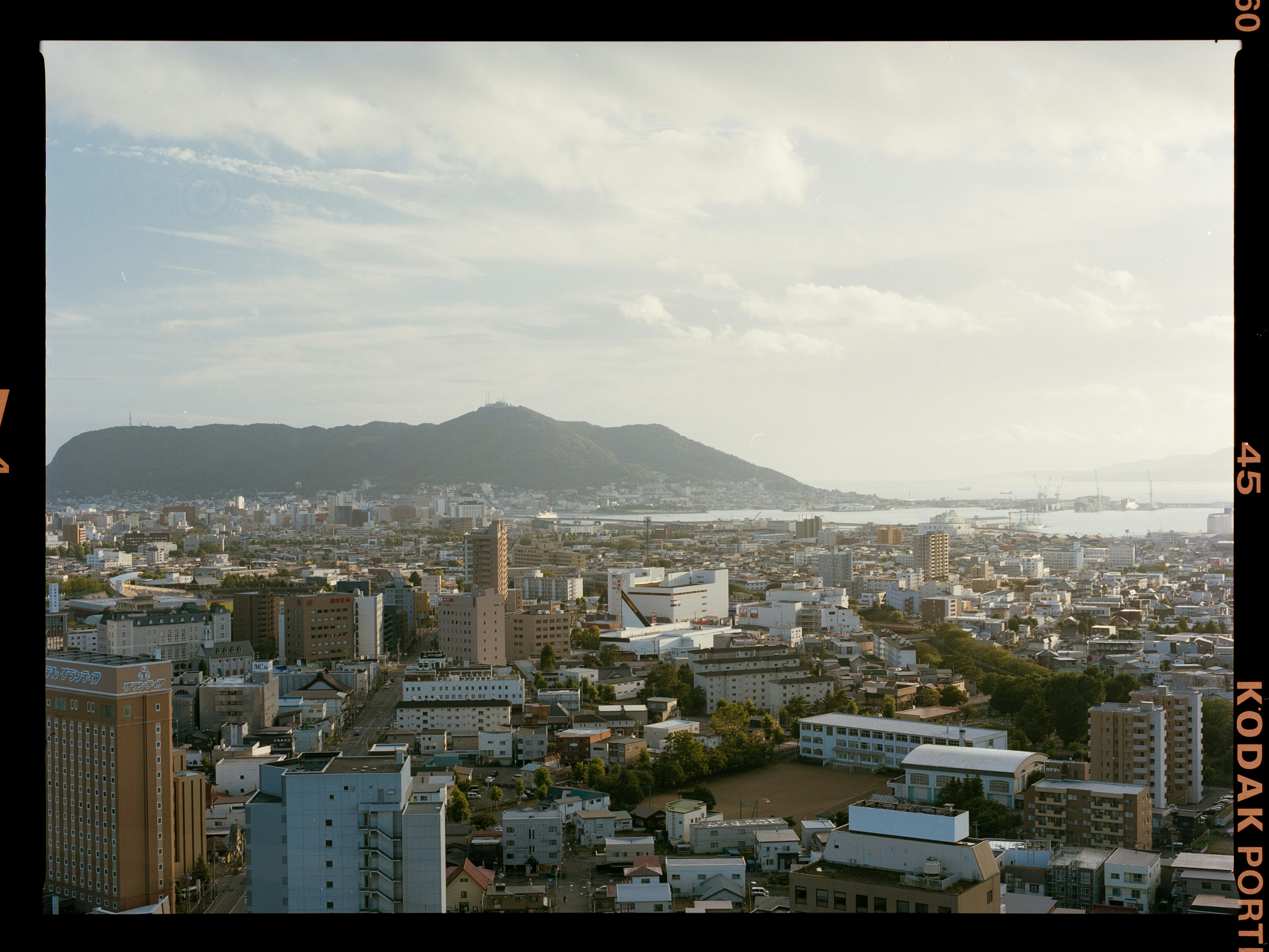 🎞️ Kodak Professional Portra 160｜🧪 Fuji Hunt C-41｜🖨️ EOS R6 + RF 100mm f/2.8L Macro｜📷 Mamiya 645 Pro + Mamiya-Sekor 80mm 1:1.9 | Cityscape with mountain and ocean in the distance