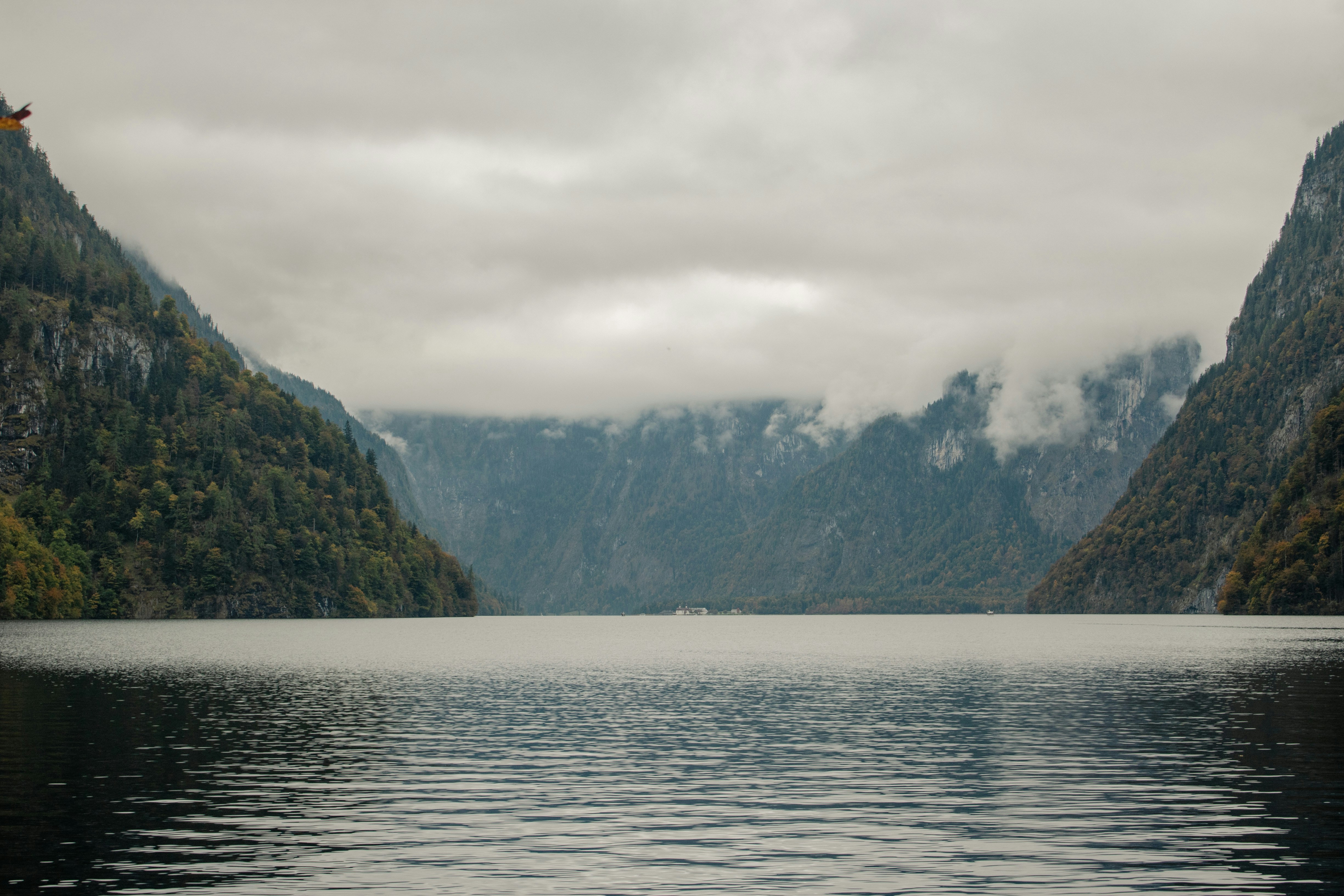 Calm lake between misty, forested mountains under cloudy sky