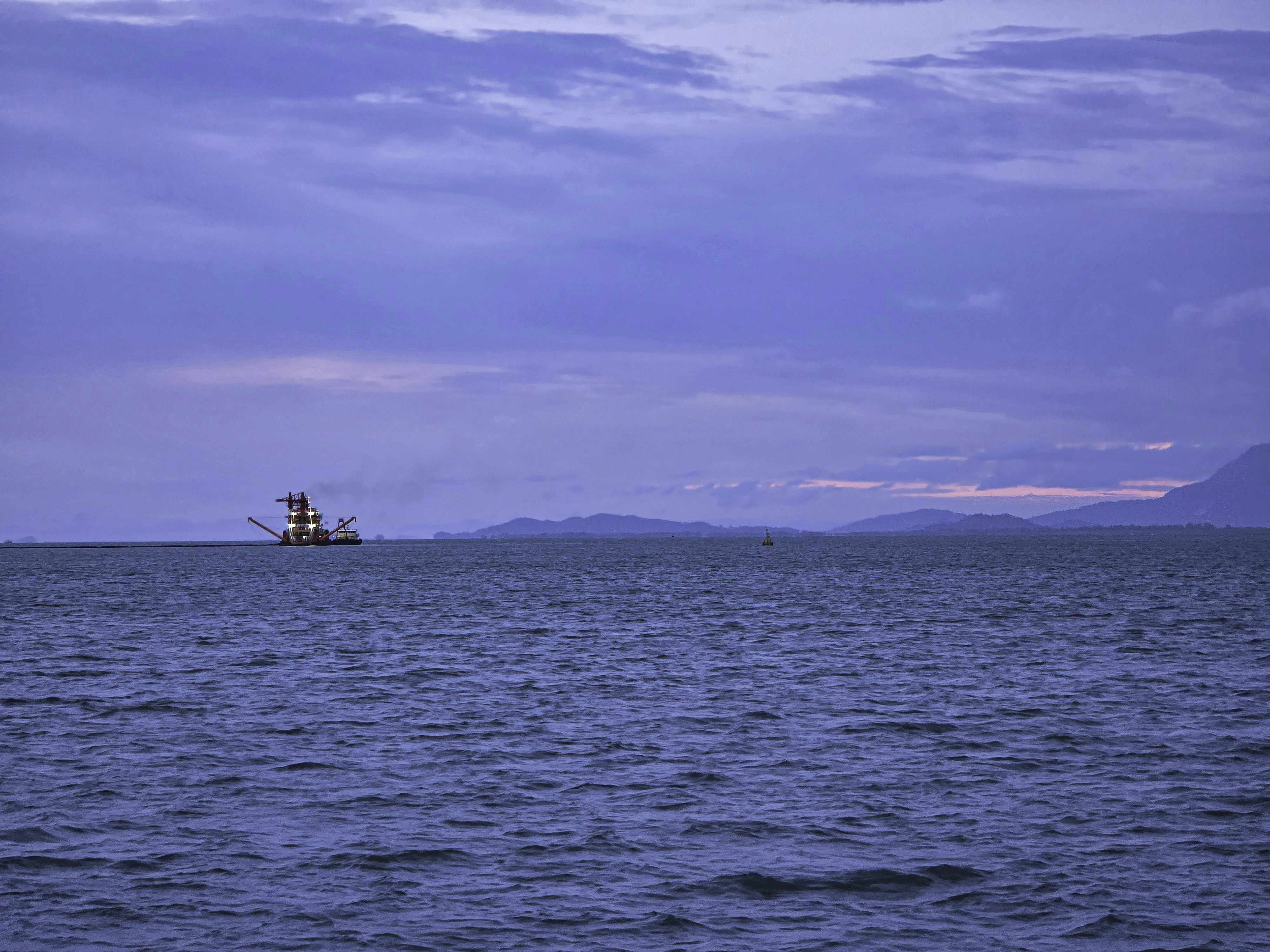 Oil rig at Sea near Penang, Malaysia | A distant ship sails on the ocean at dusk.