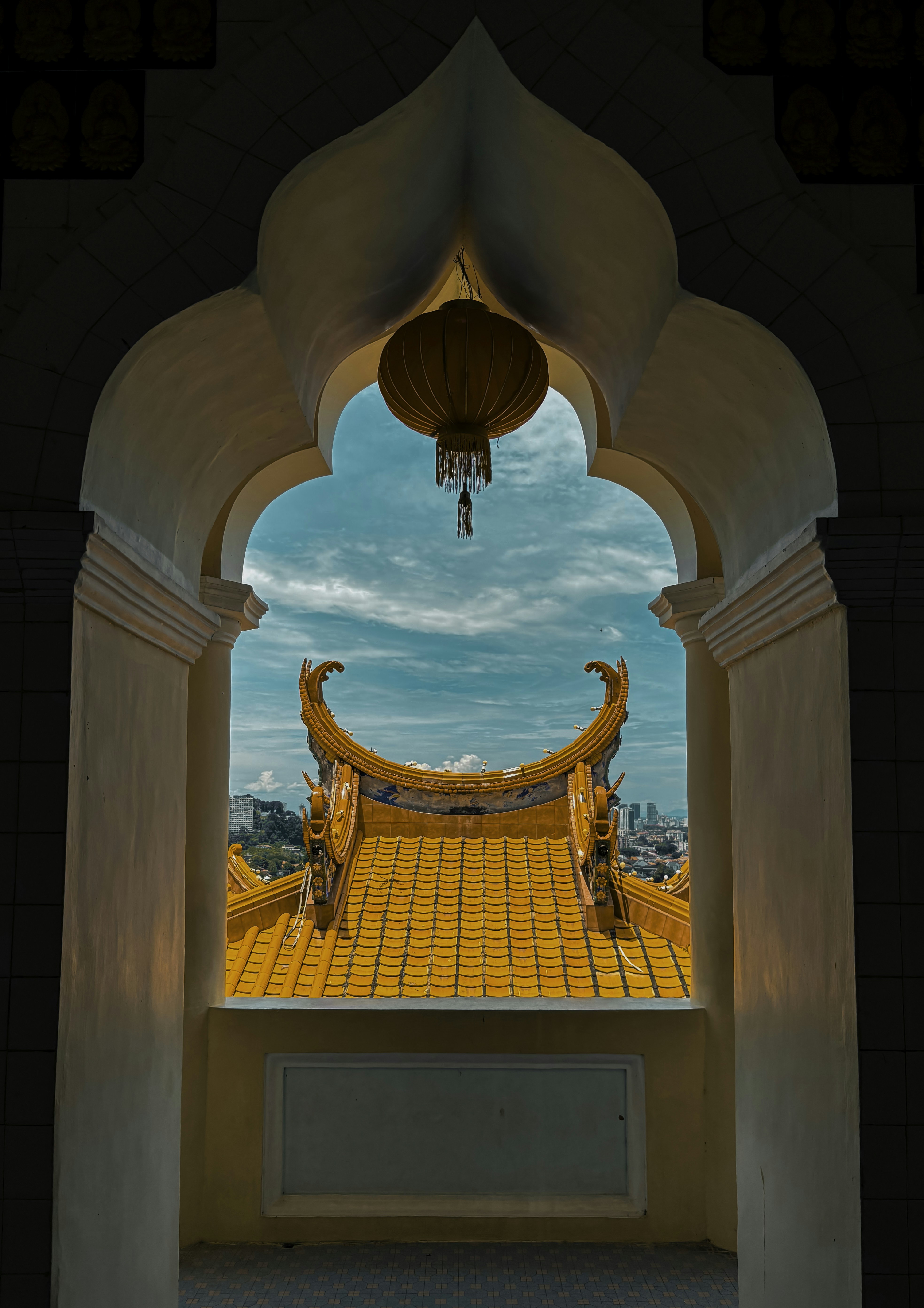 View through an ornate archway showcasing a vibrant yellow temple roof against a backdrop of a cloudy sky.