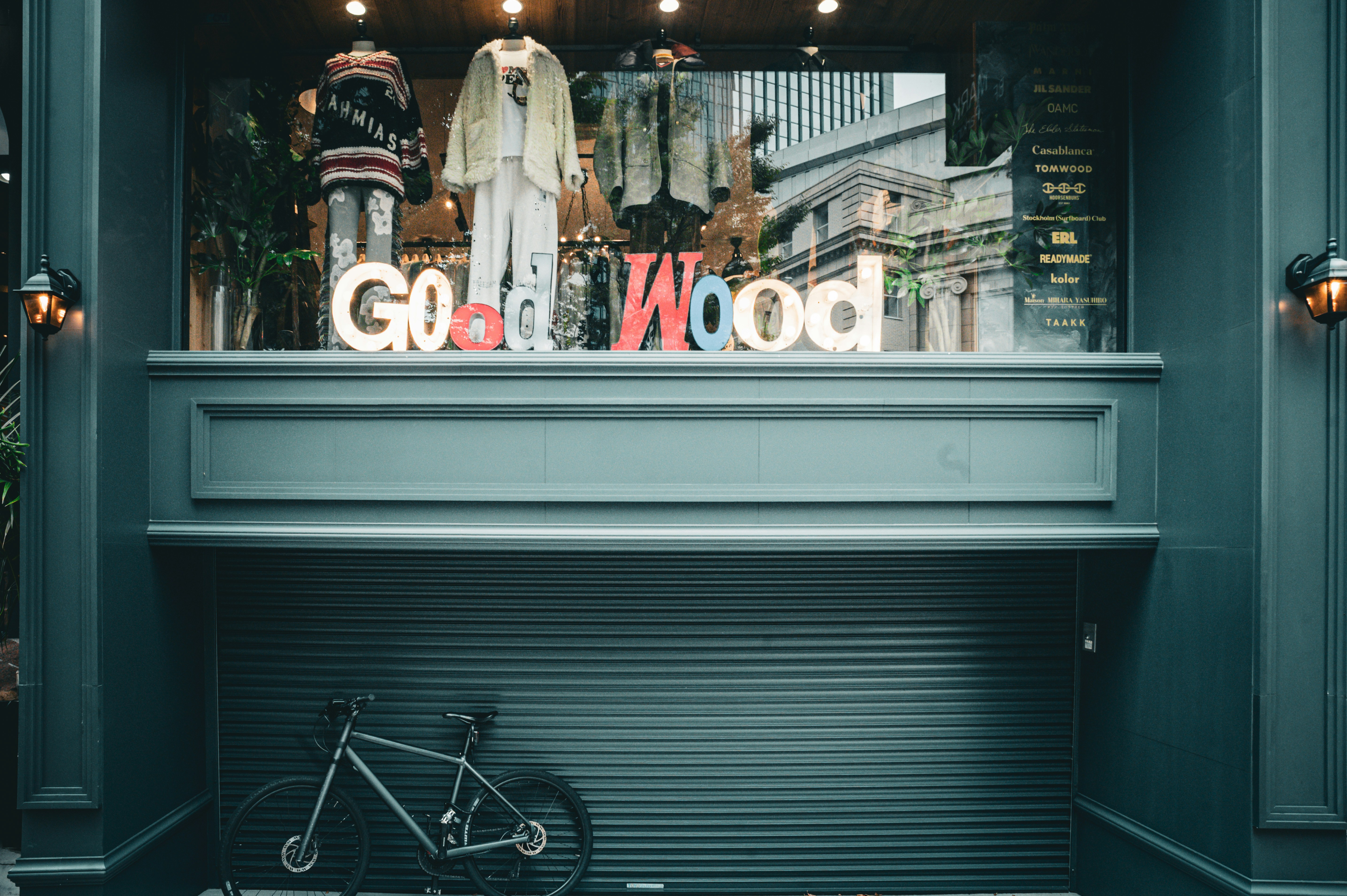 Boutique storefront showcasing stylish clothing with illuminated signage and a bicycle parked in front. The aesthetic blends contemporary design with urban charm.