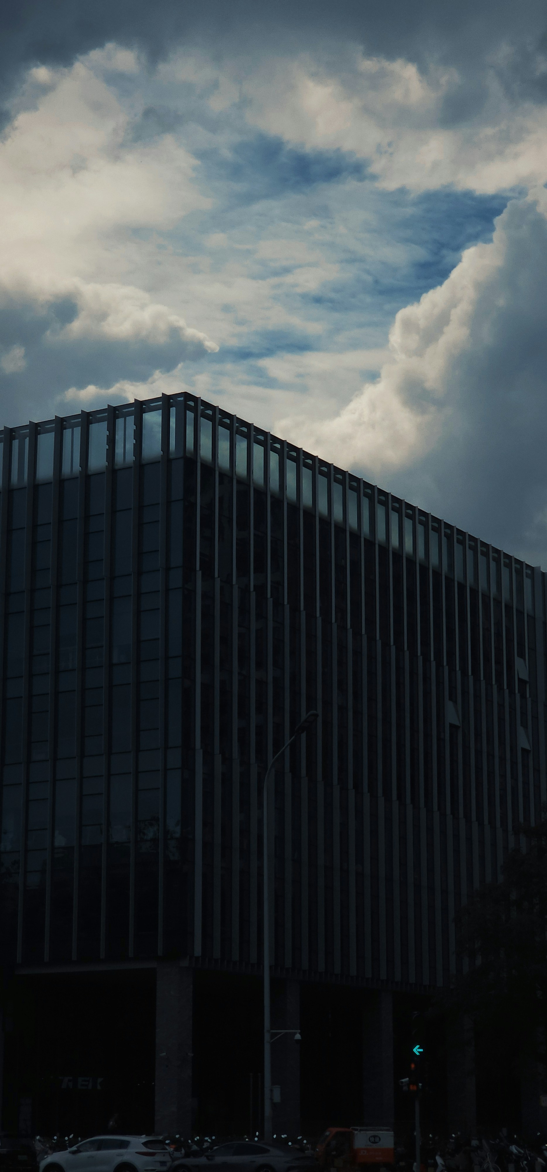 A sleek, modern building with glass panels reflecting the cloudy sky above, capturing the contrast between architecture and nature.