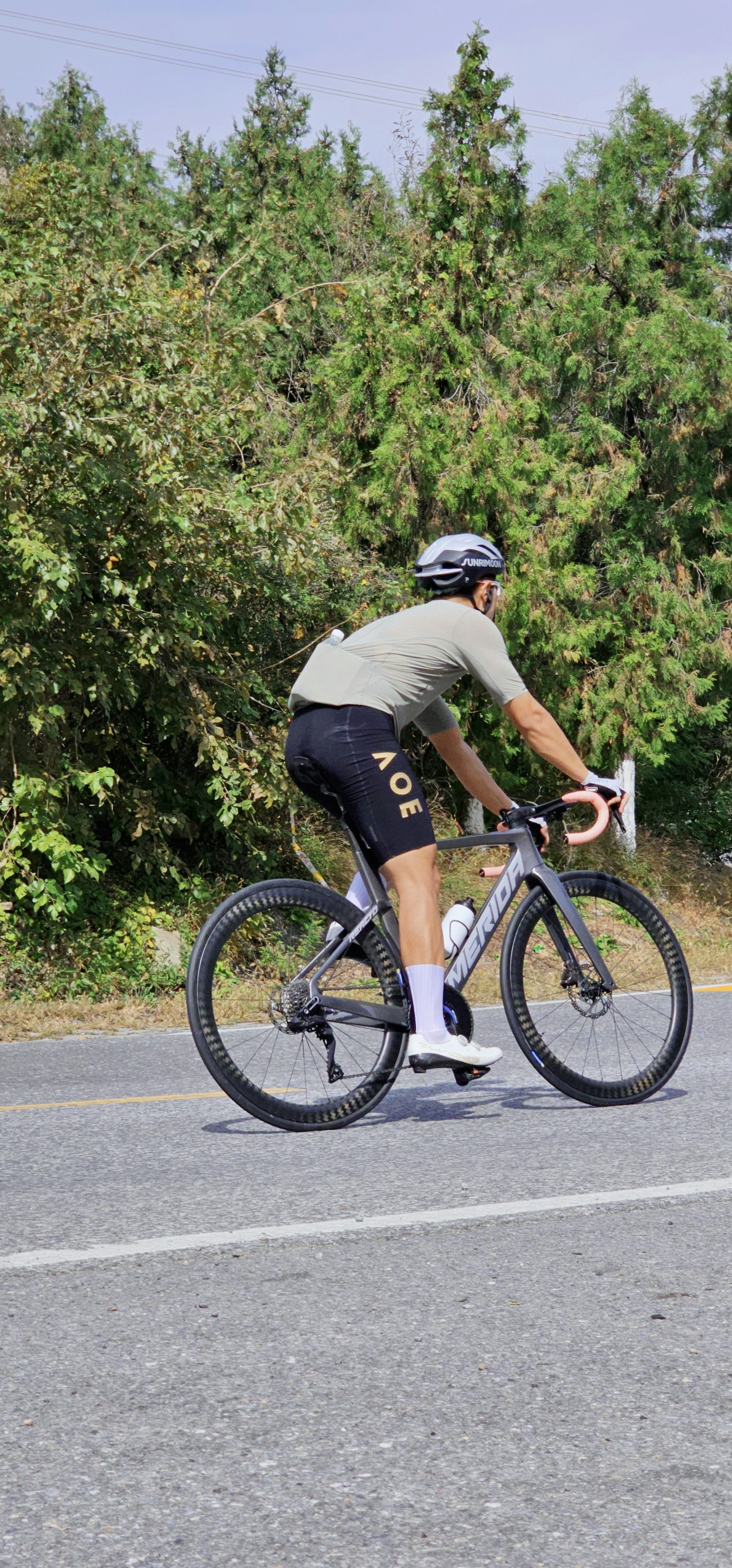 Man cycling on a road with trees behind him