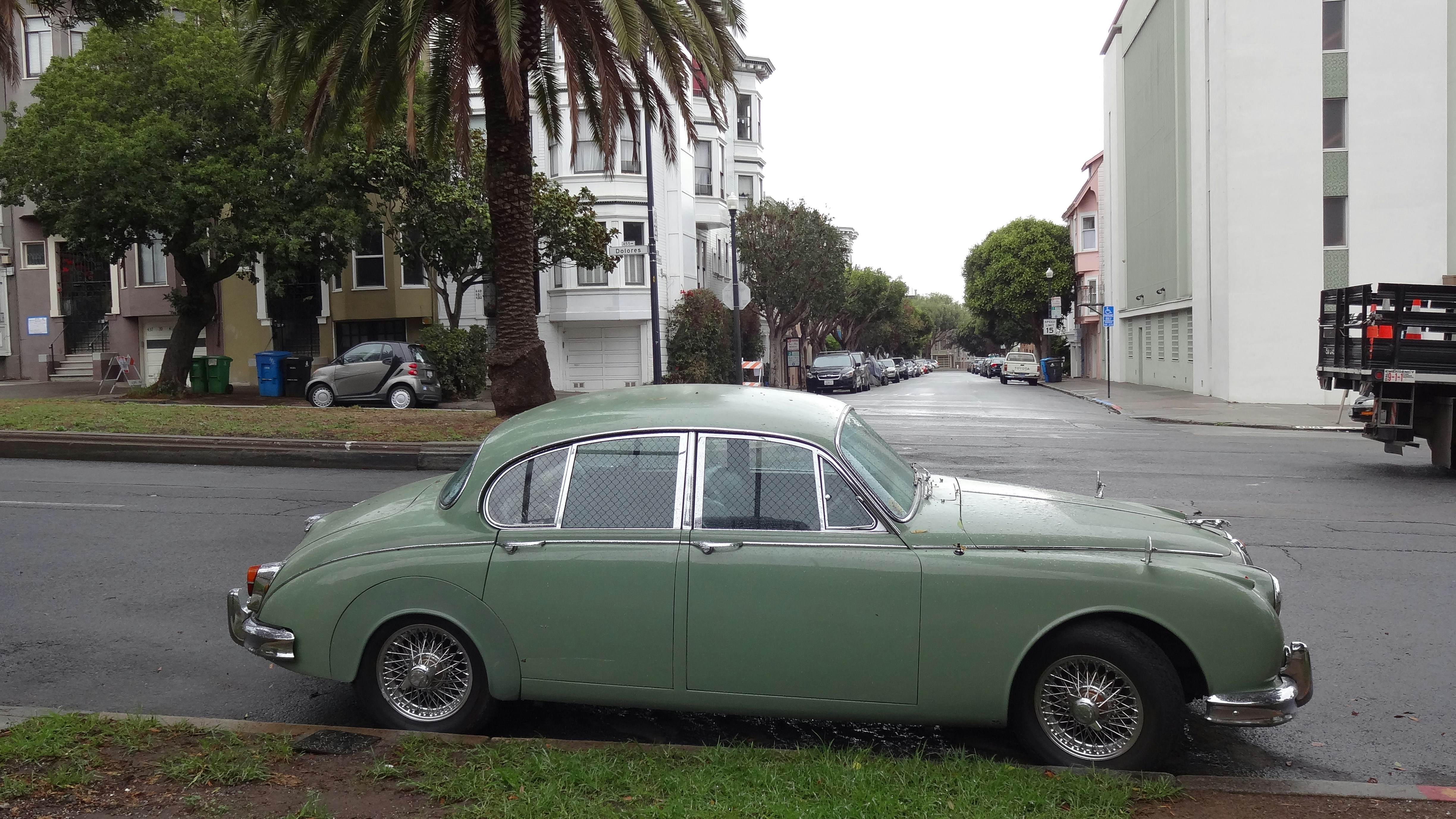 Classic green sedan parked along a tree-lined street, showcasing a blend of vintage design against a modern backdrop.