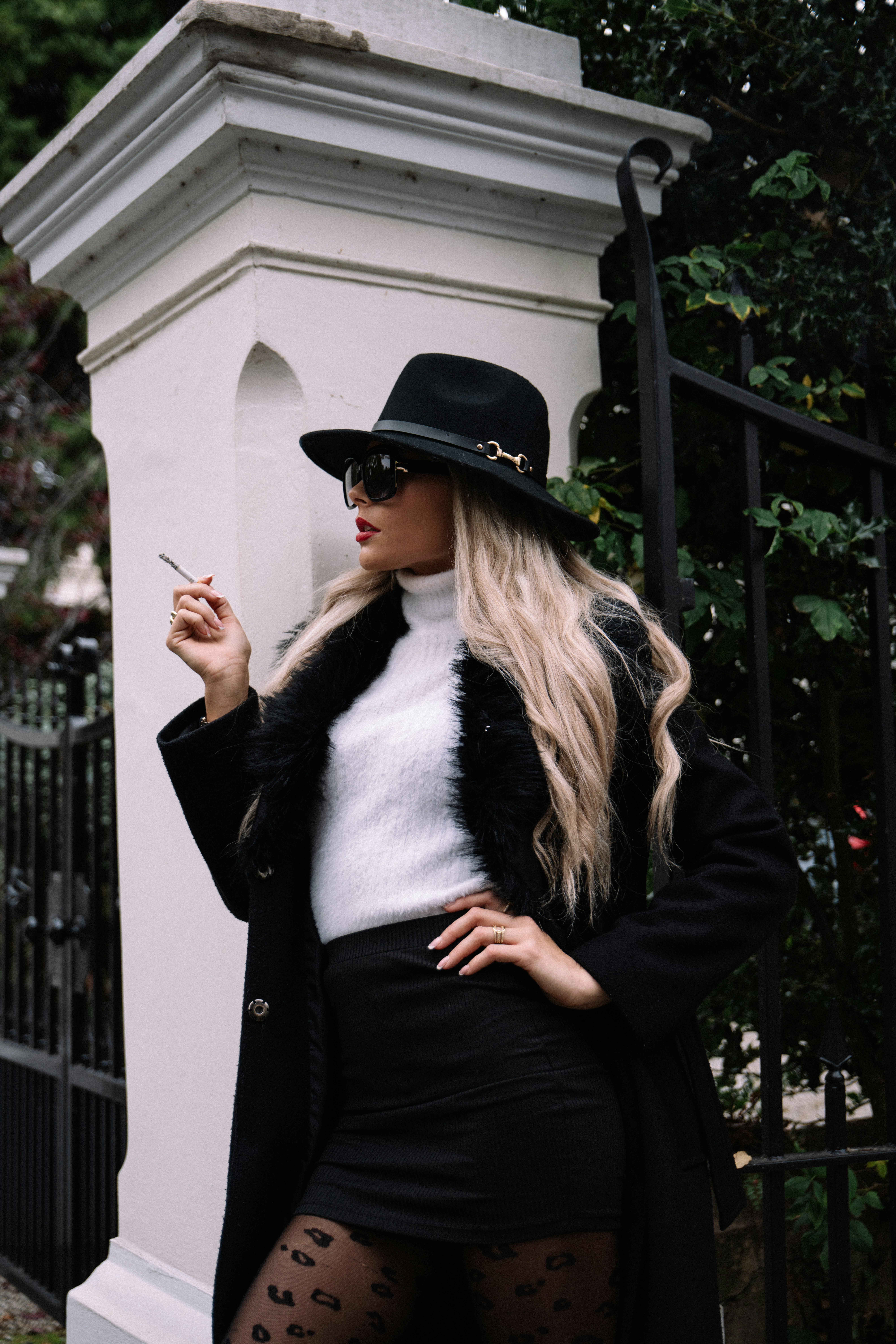 Woman in hat and coat smoking a cigarette outdoors.